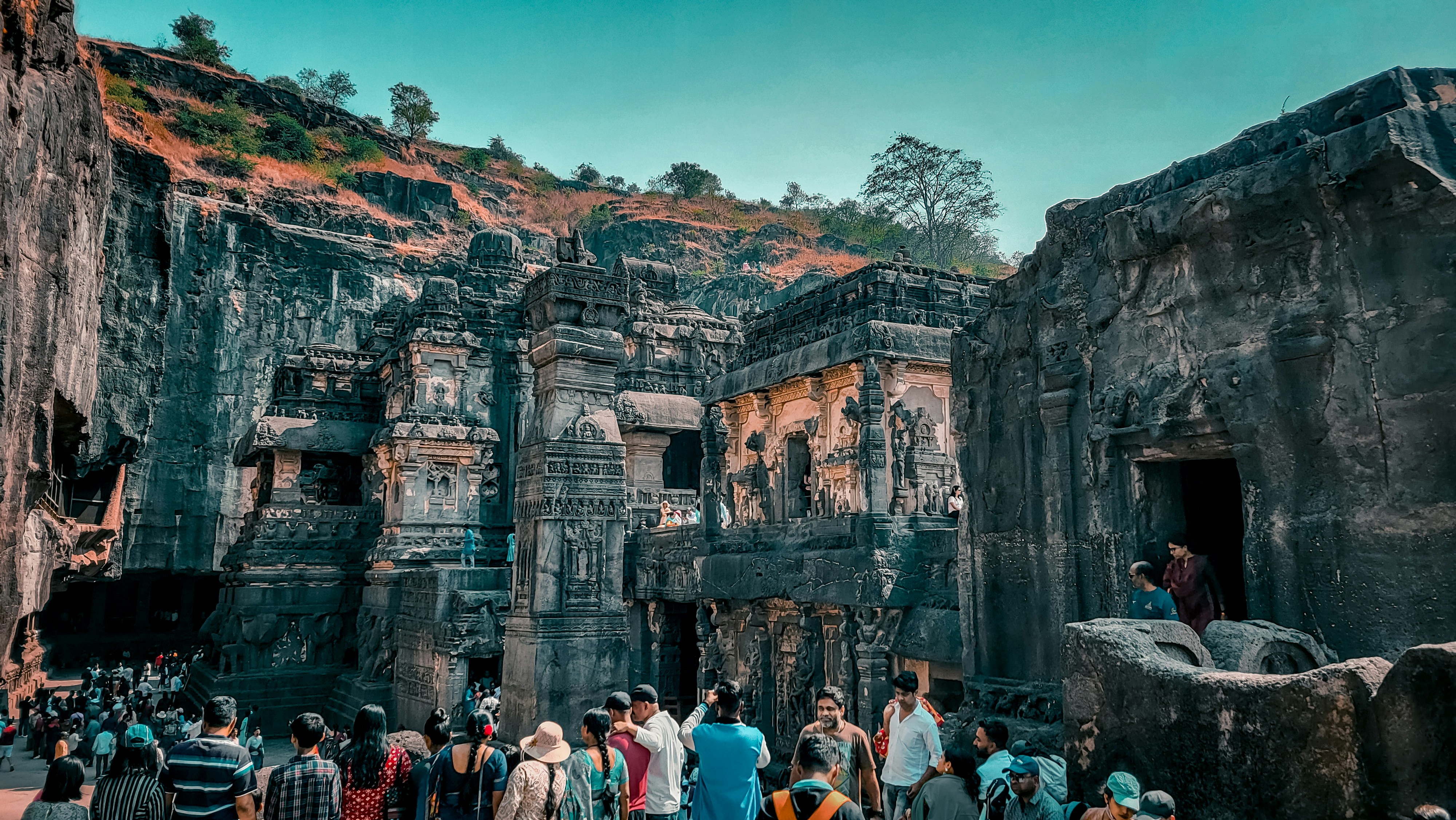 Stone Choir Under Teal Sky: Visitors Among Ancient Temple Carvings