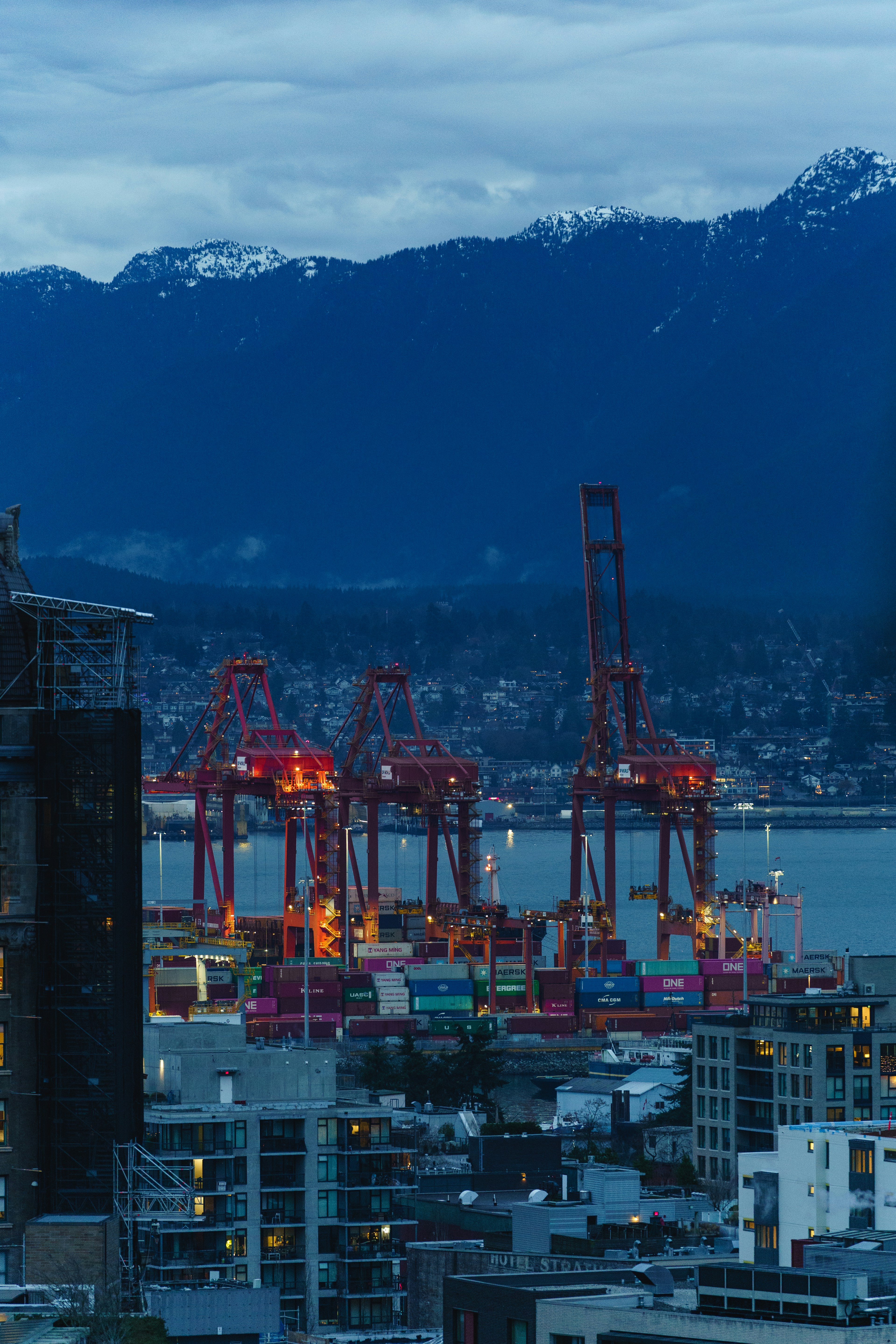 Neon cranes and distant coastline under a blue evening veil