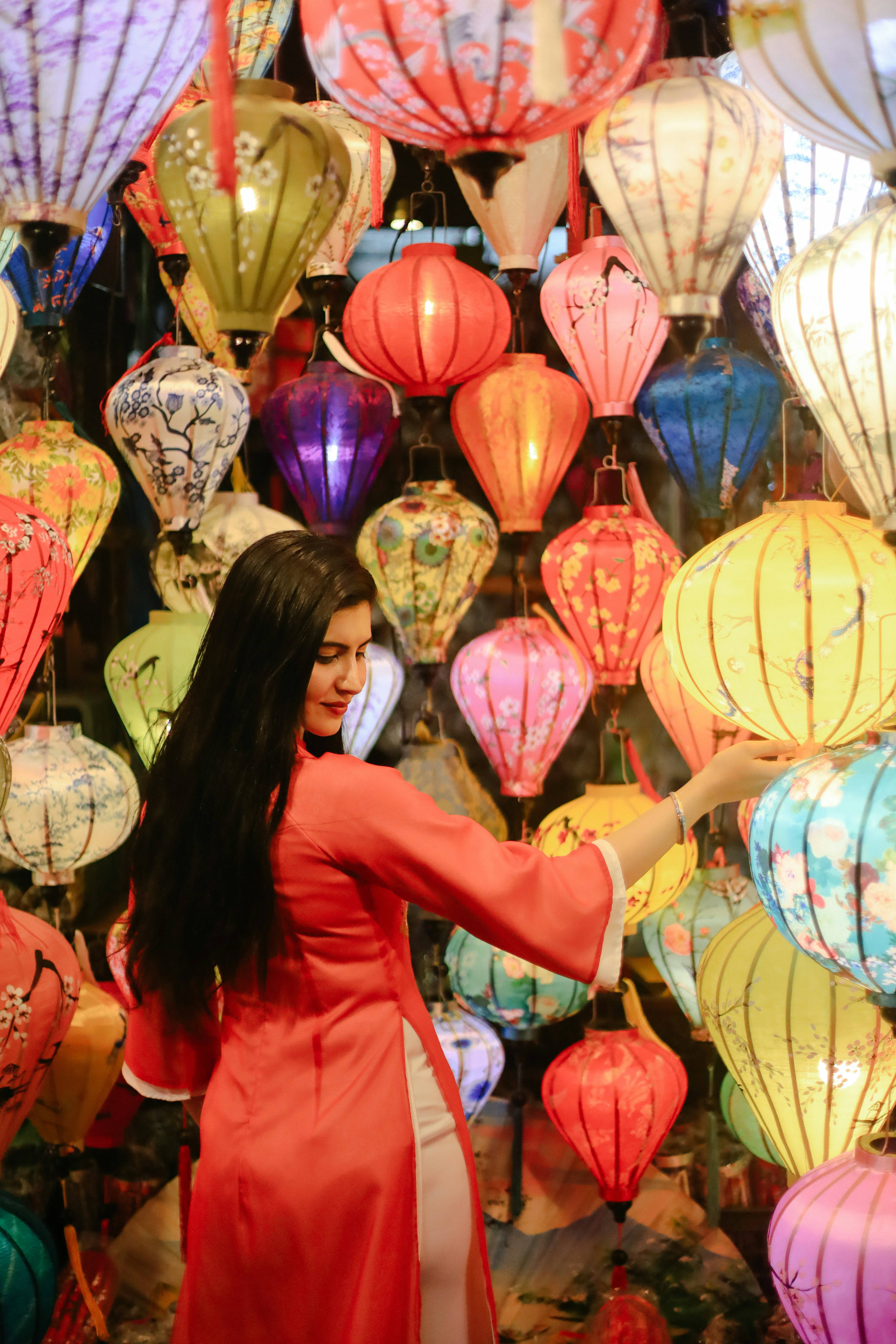A woman in a red dress standing in front of many colorful lanterns ...