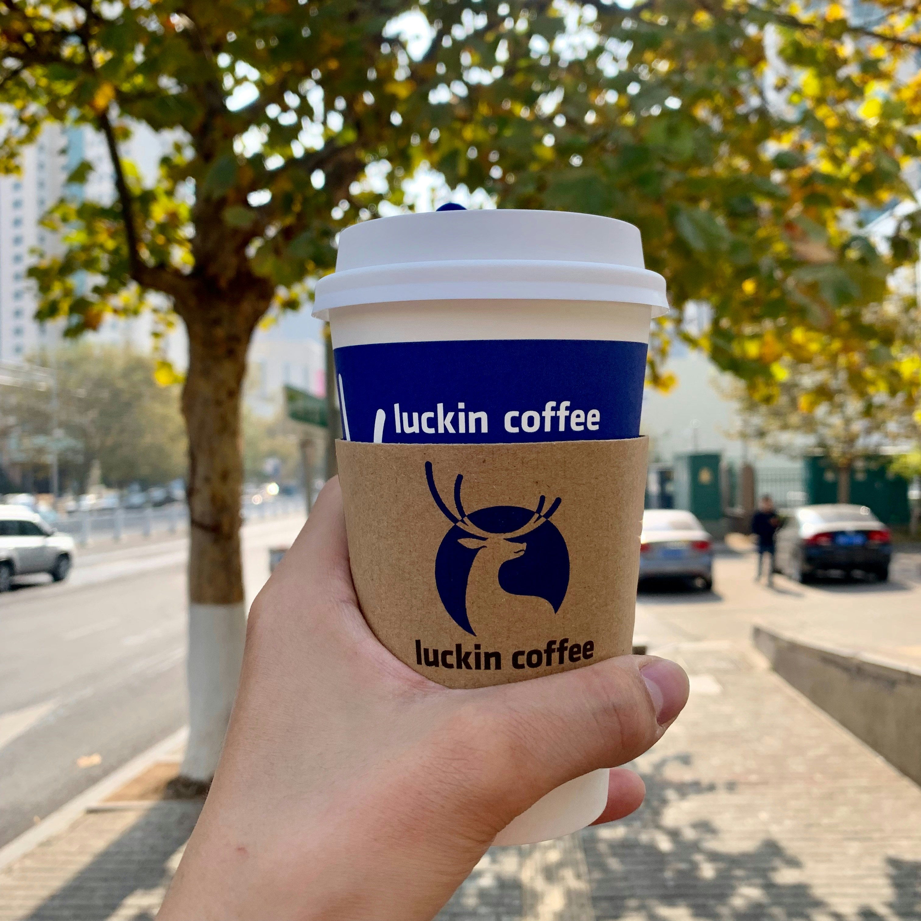 Urban warmth at arm's length: a Luckin coffee on a sunlit sidewalk