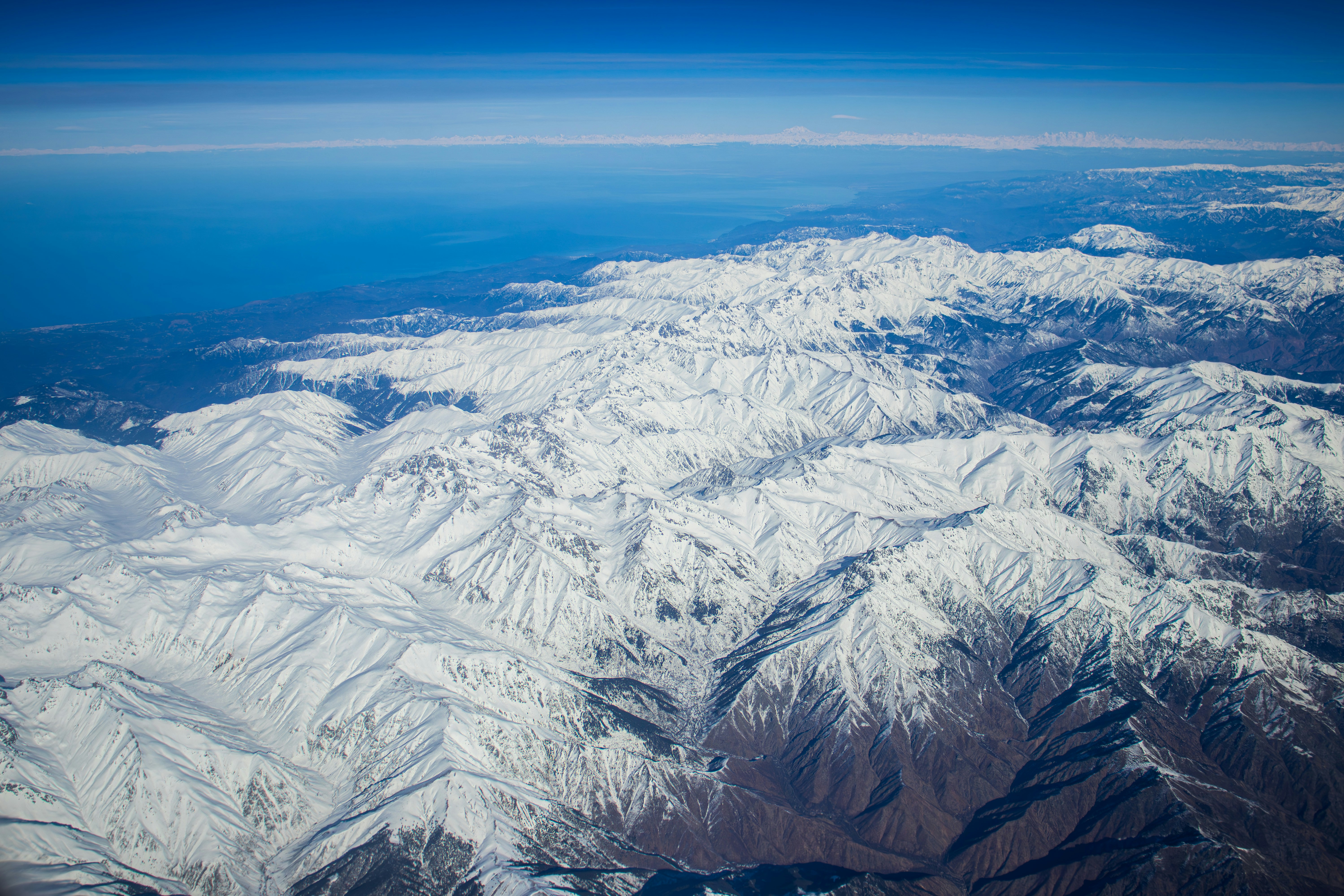 Aerial view of snow-covered mountain range under a clear blue sky.