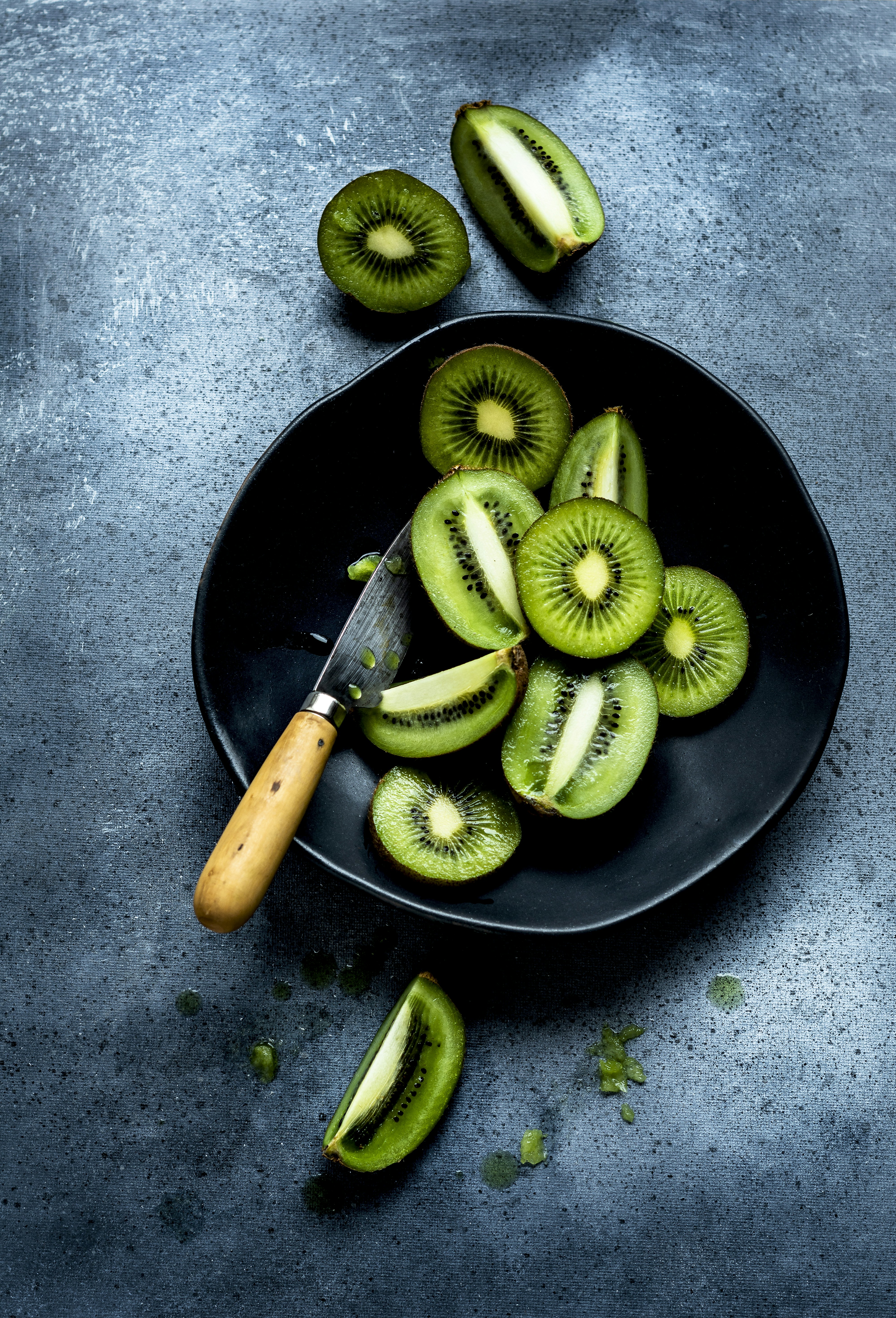 a black plate topped with sliced kiwis and a knife