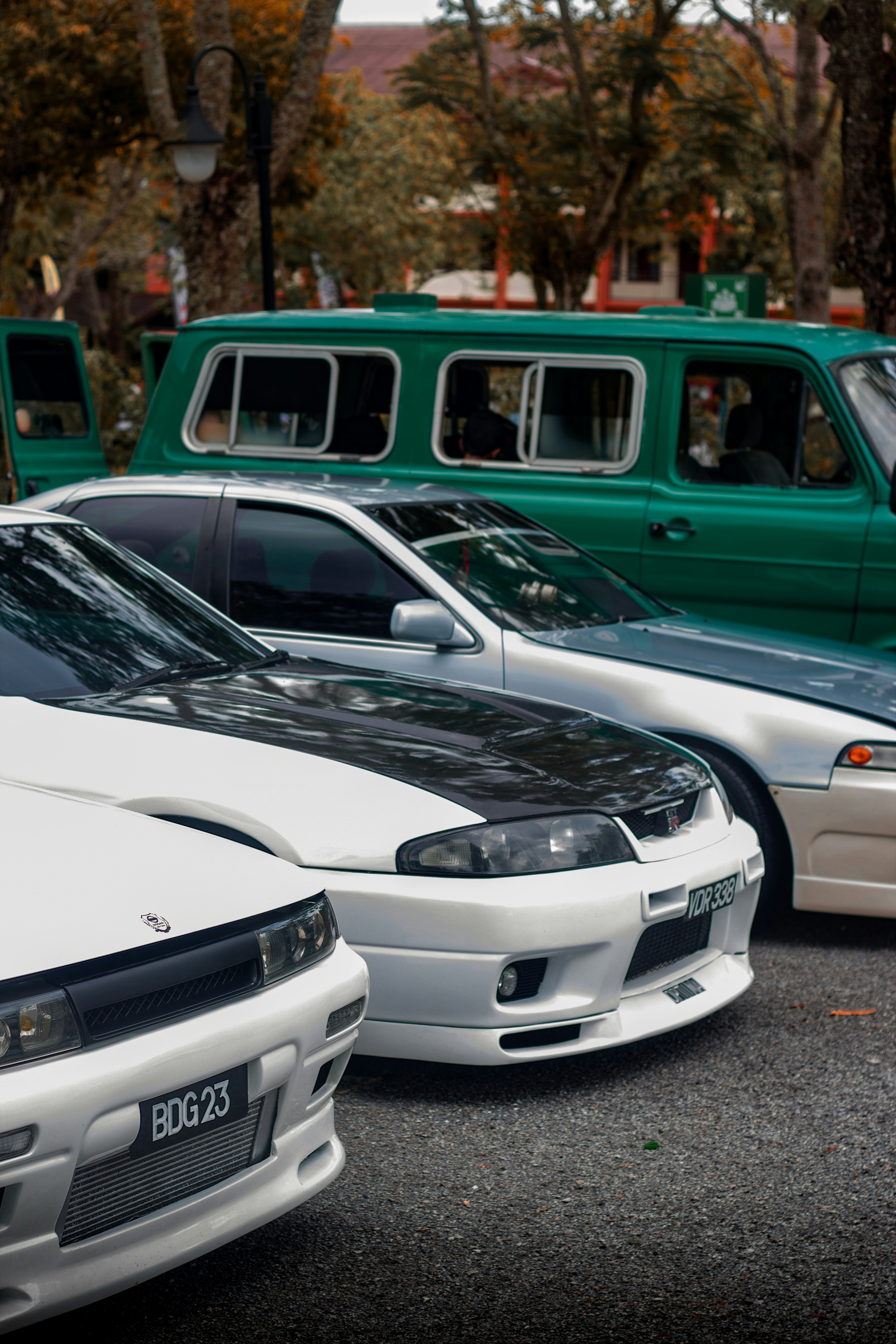 Three distinct cars parked in a vibrant setting, showcasing their unique designs and colors against a backdrop of trees and a green vehicle.
