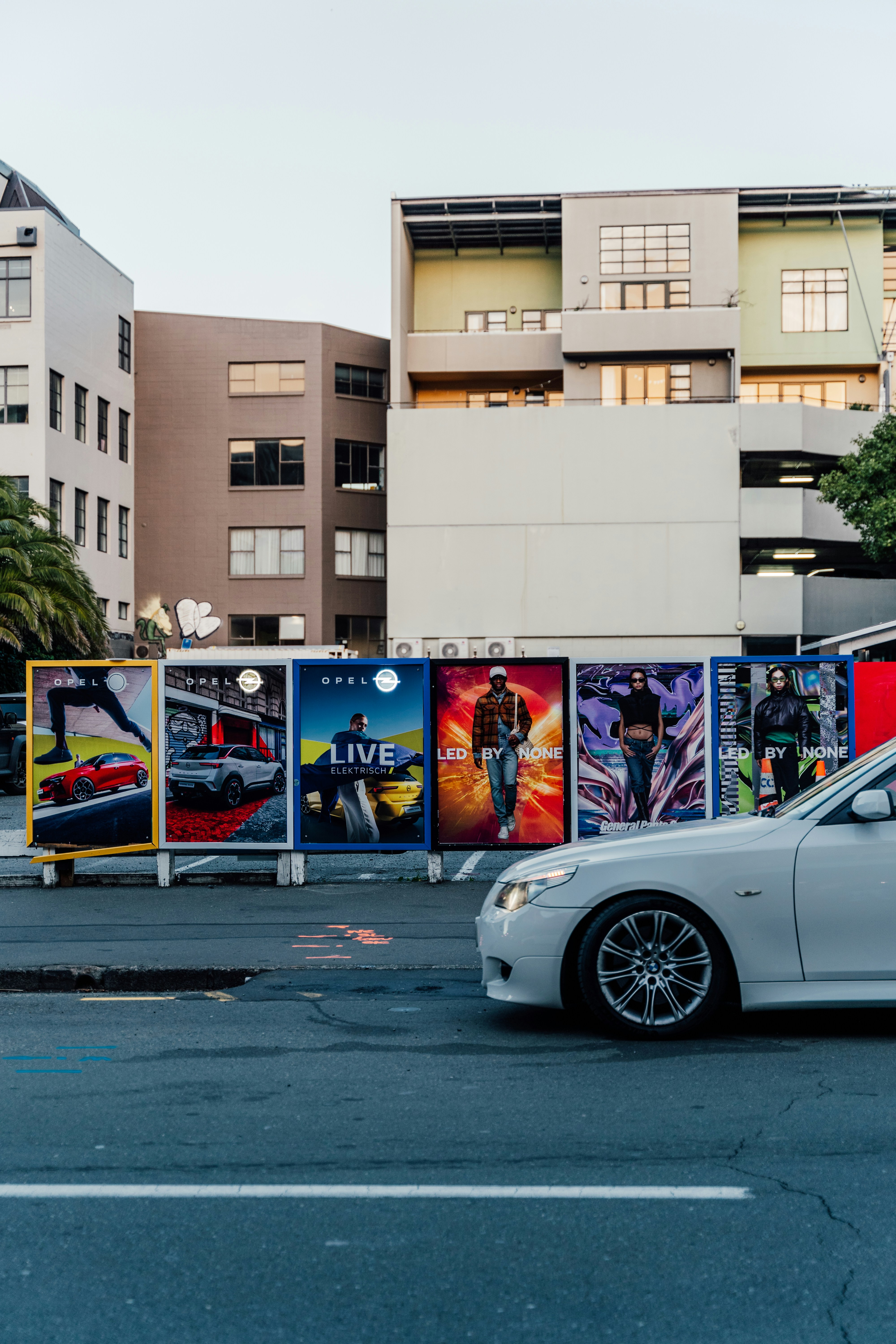 Street-side Poster Wall with Car in Foreground, Urban Apartments Behind