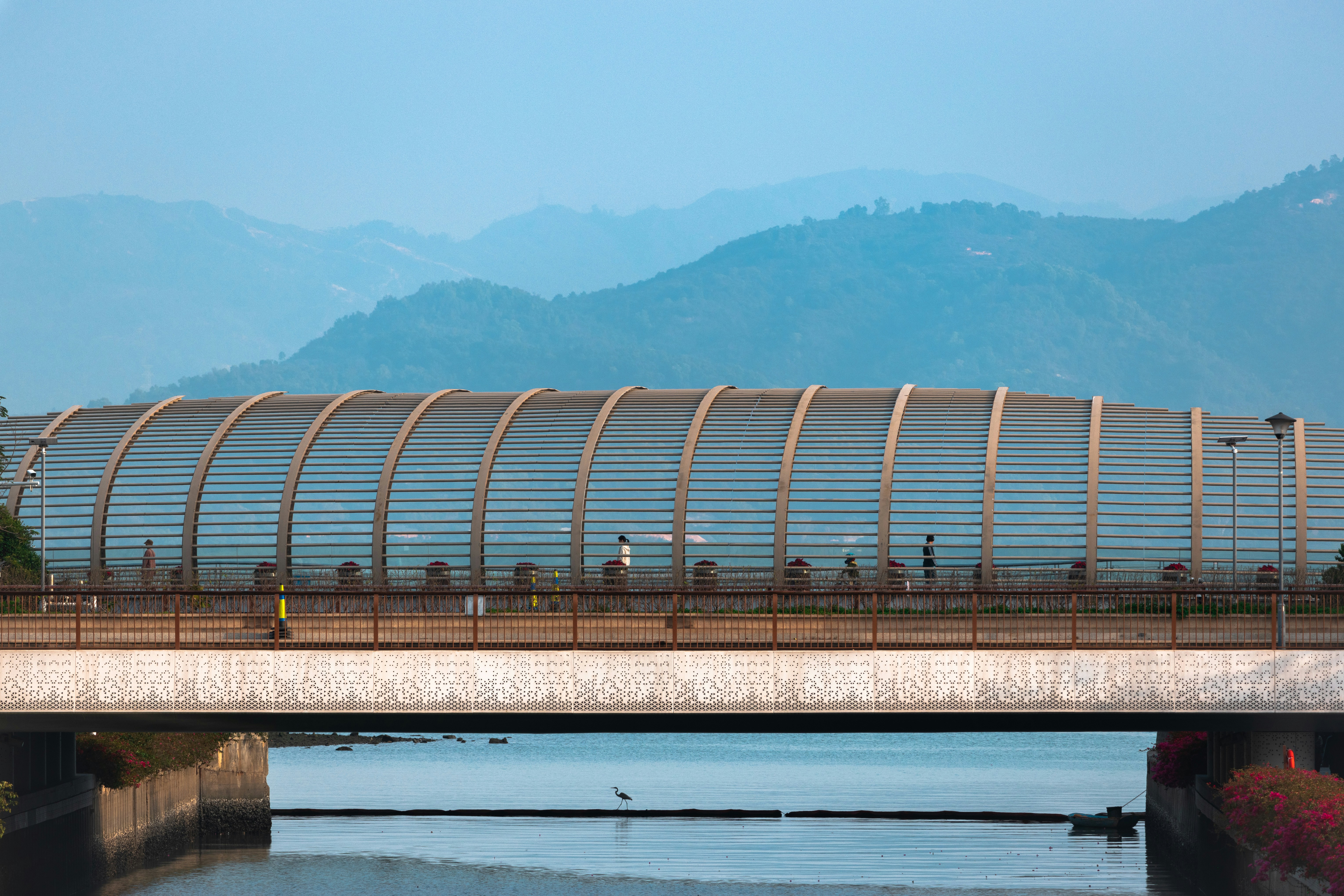 Ribbed Canopy Bridge Over a Calm River, Framed by a Misty Blue Mountain Range