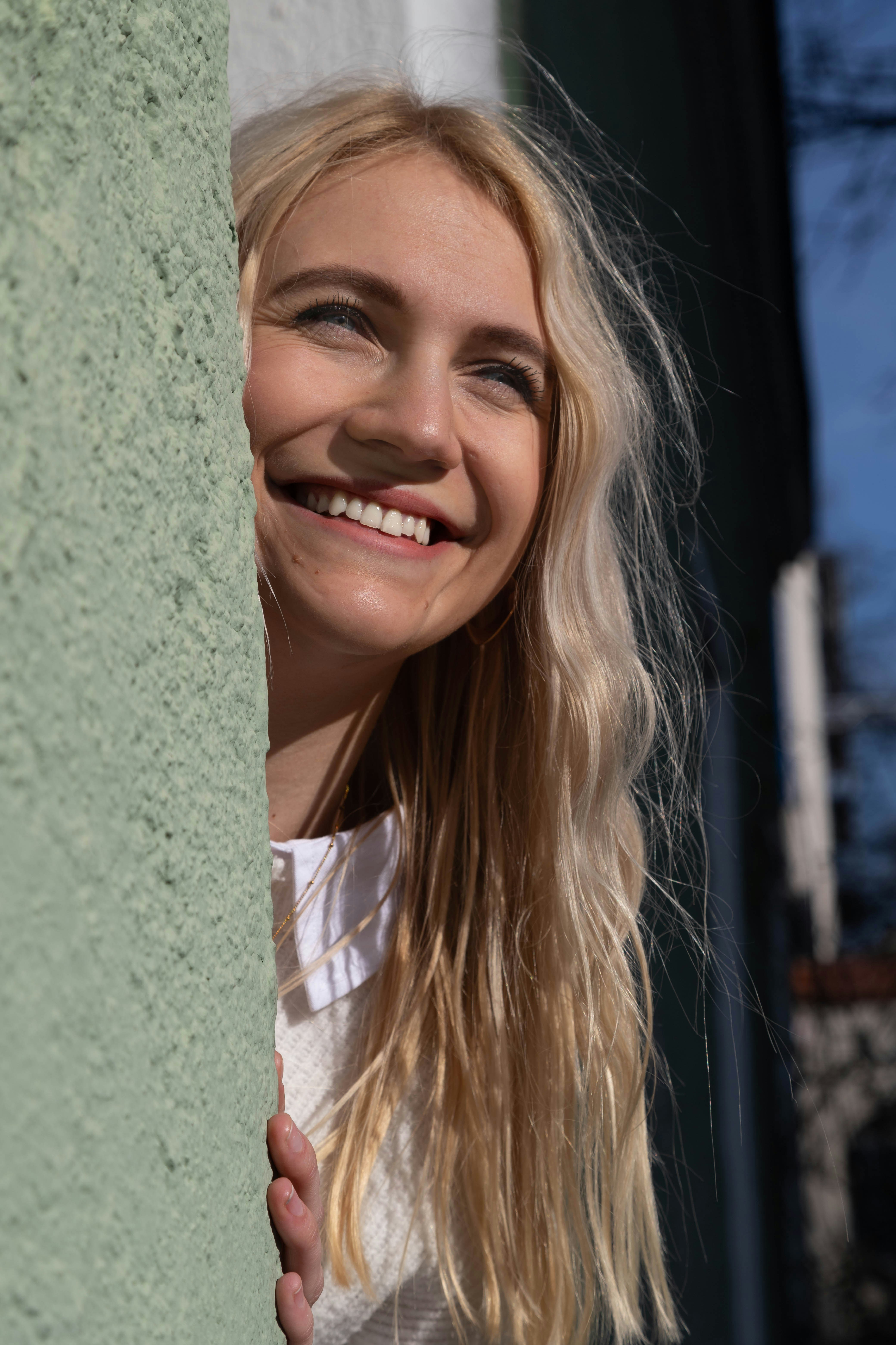 A woman with blonde hair is smiling and leaning against a wall photo ...