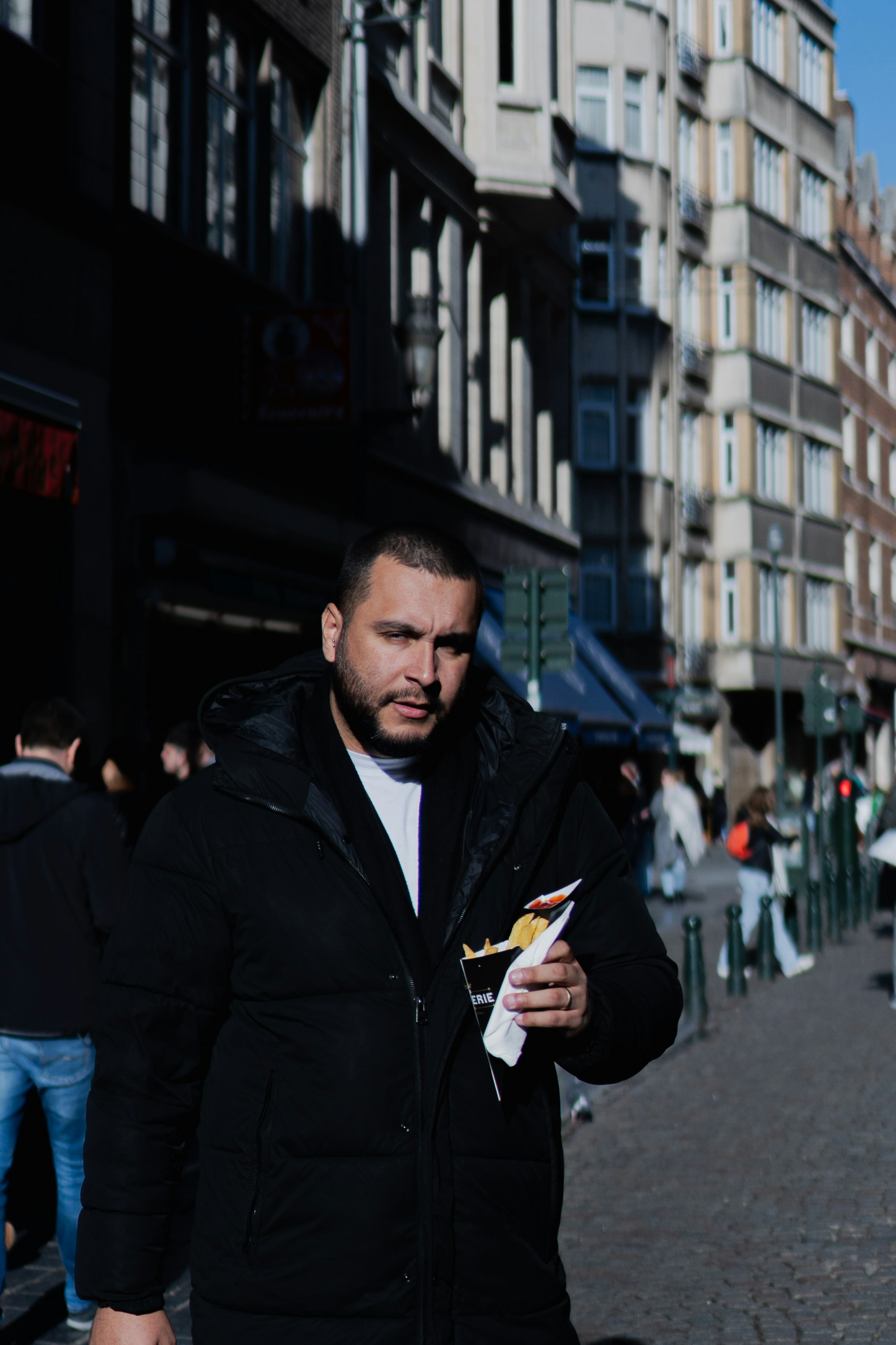 City Street Portrait: A man in a puffer jacket amid urban afternoon bustle