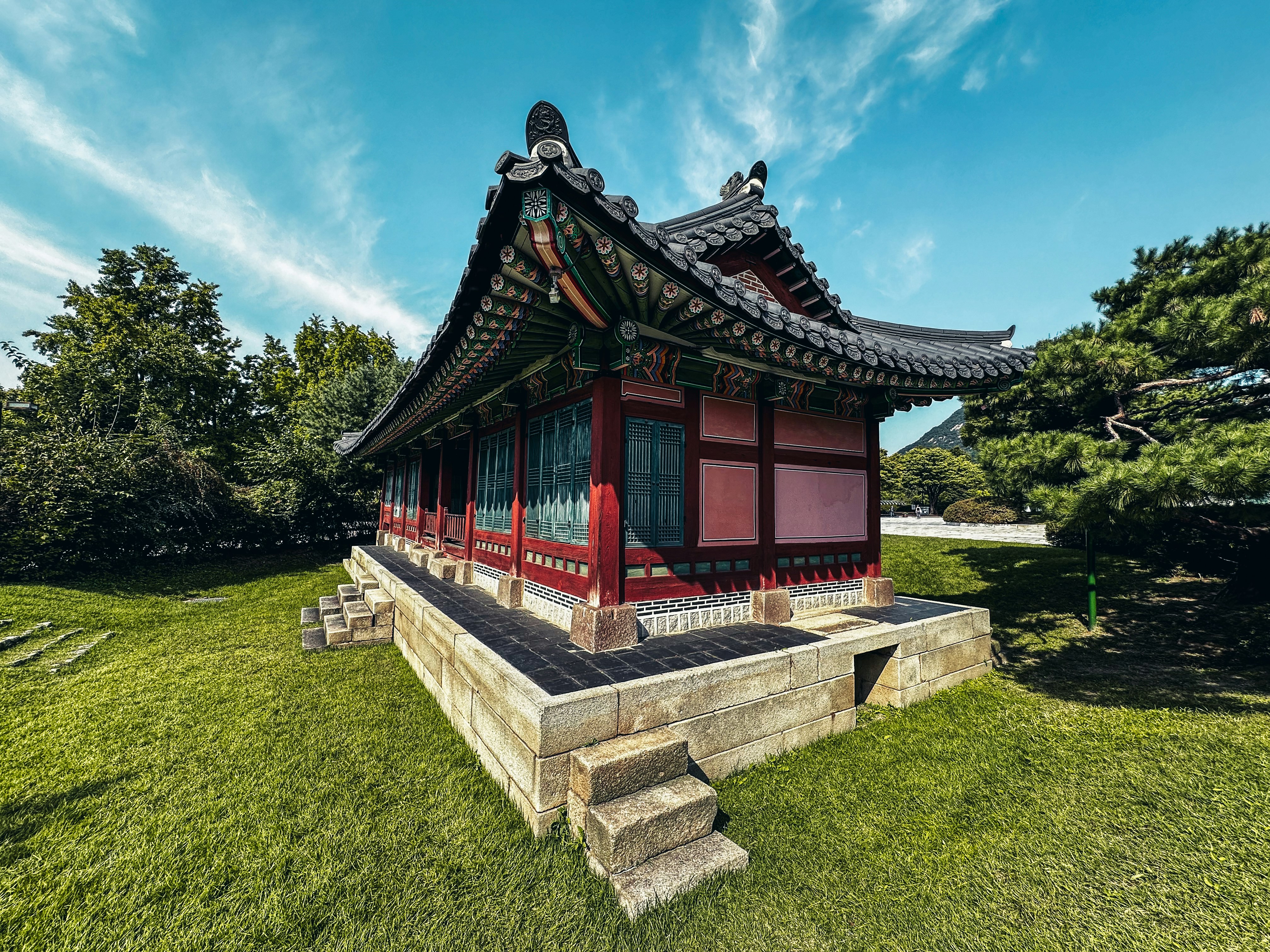 Traditional Korean structure with ornate roof set on a vibrant green lawn under a bright blue sky.