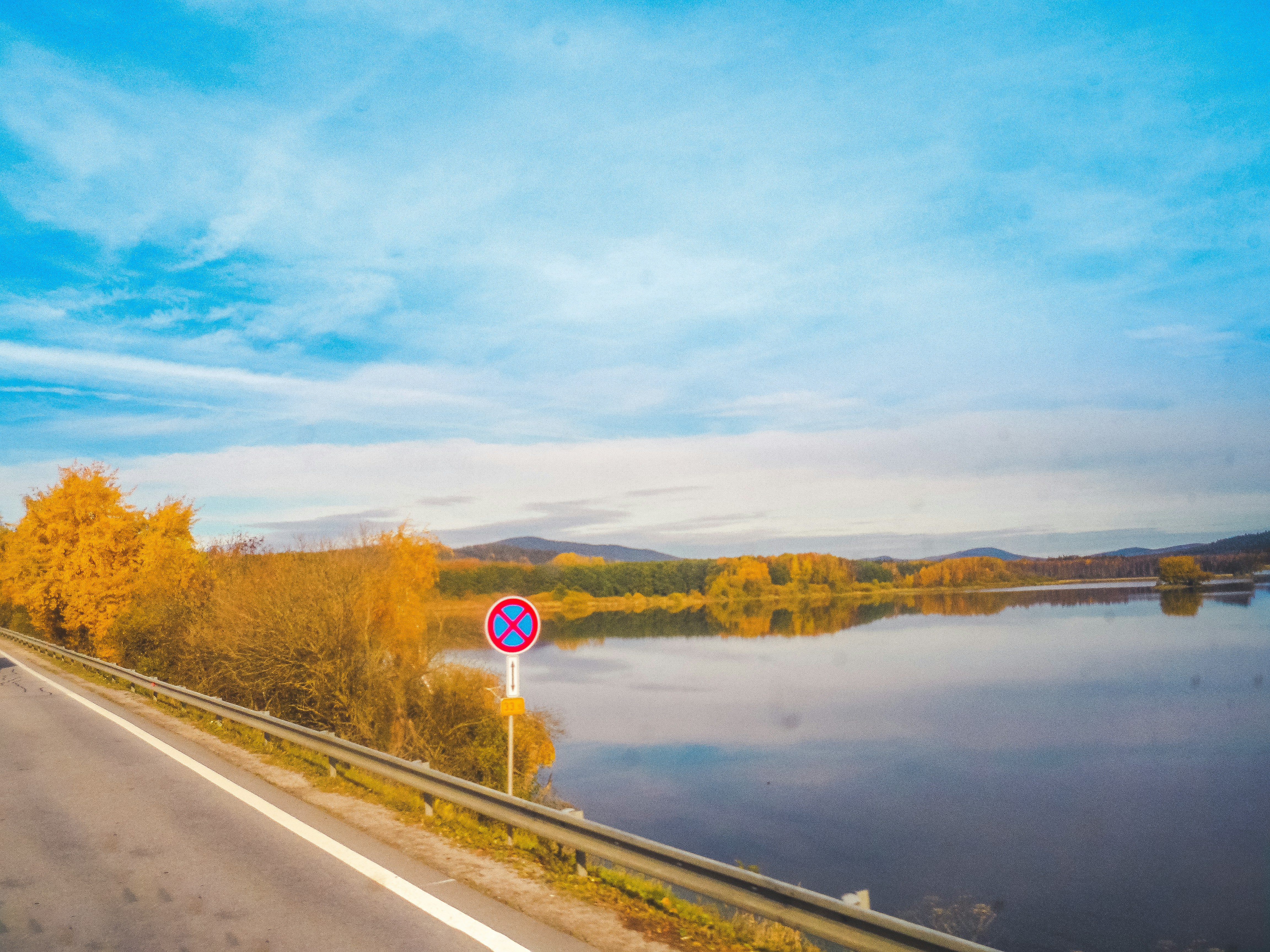 Autumn highway beside a tranquil lake under a cobalt sky