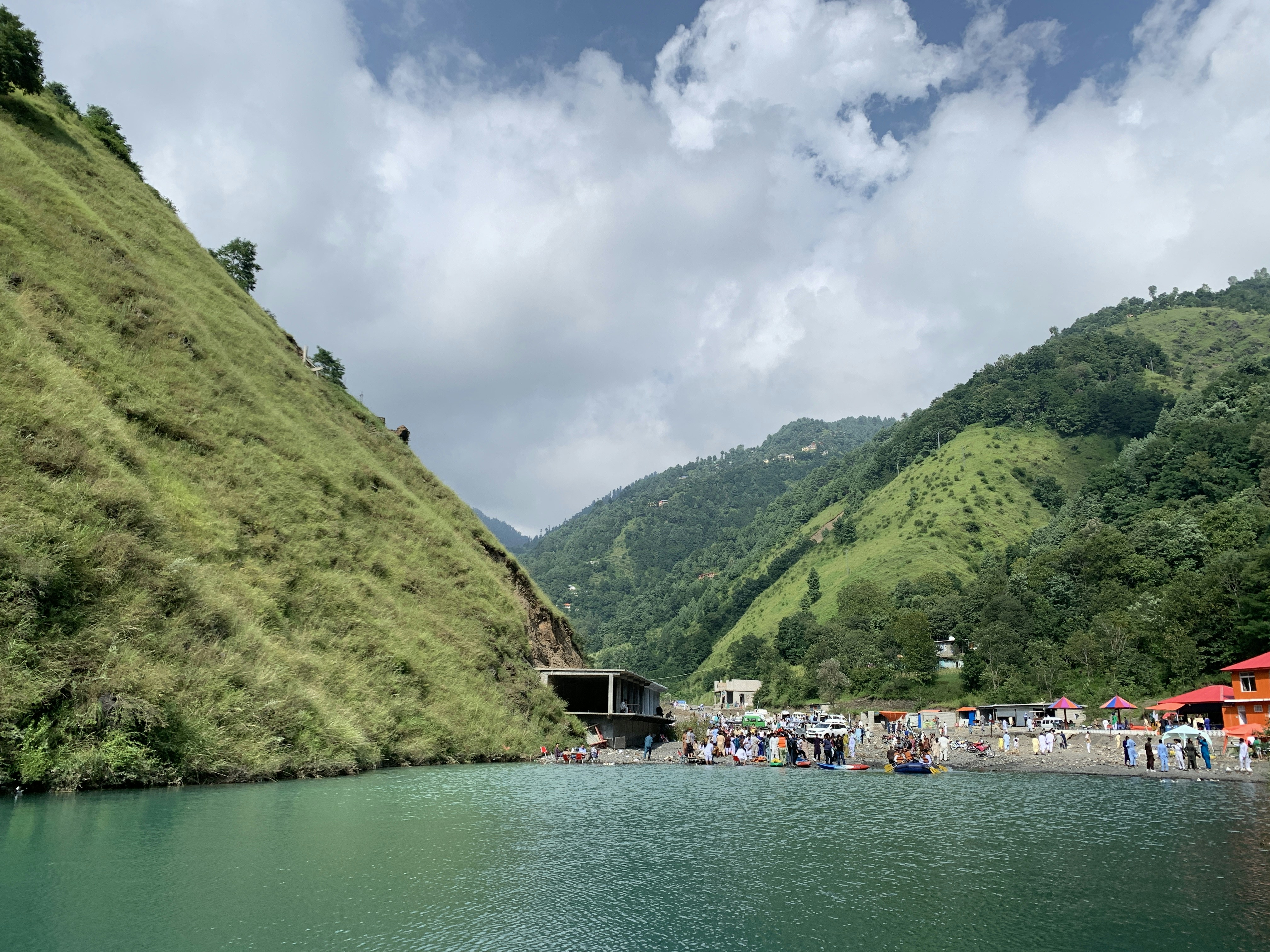 Tranquil lake nestled between lush green hills under a partly cloudy sky.