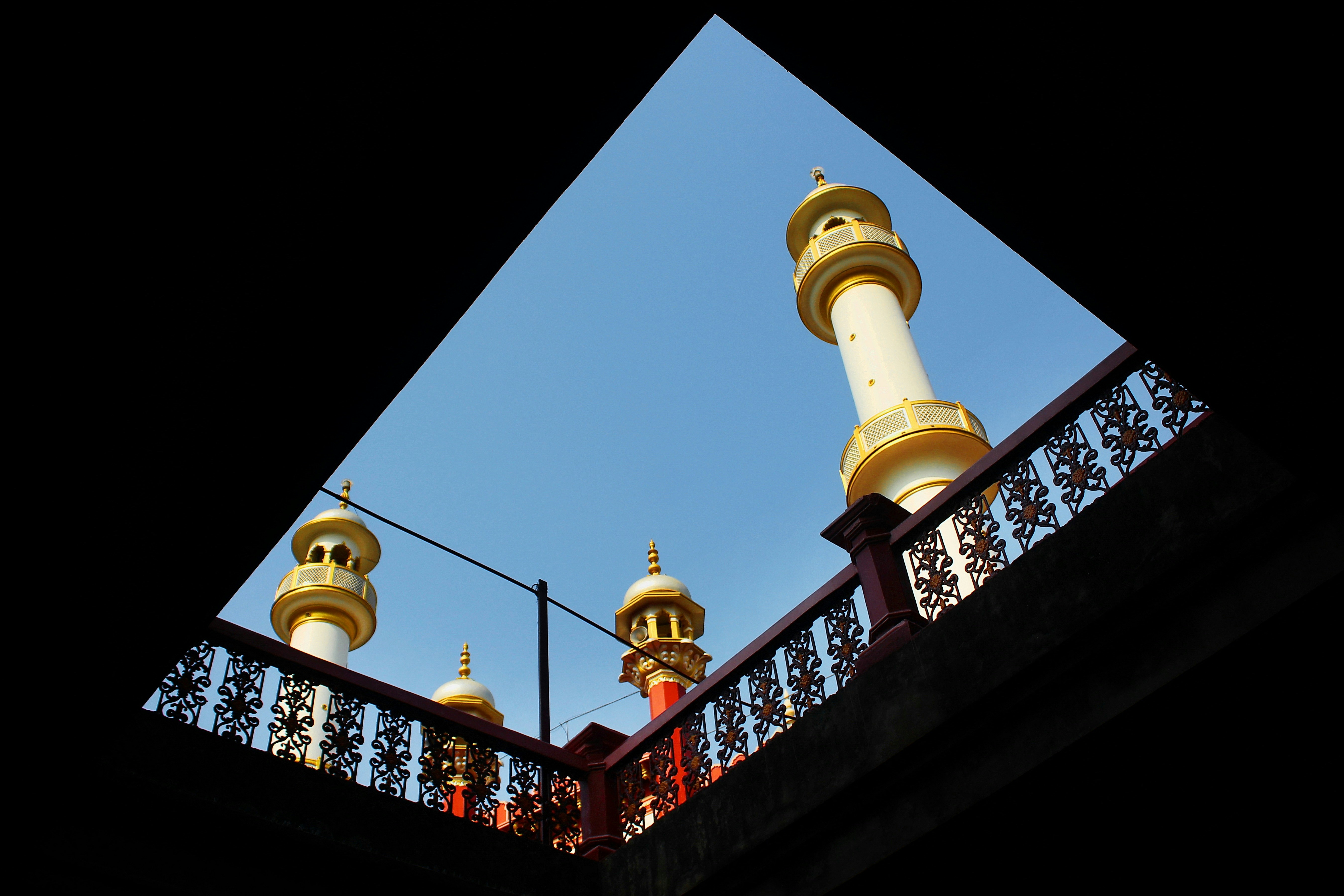 Golden minarets rise against a clear blue sky, framed by the silhouette of a courtyard opening.
