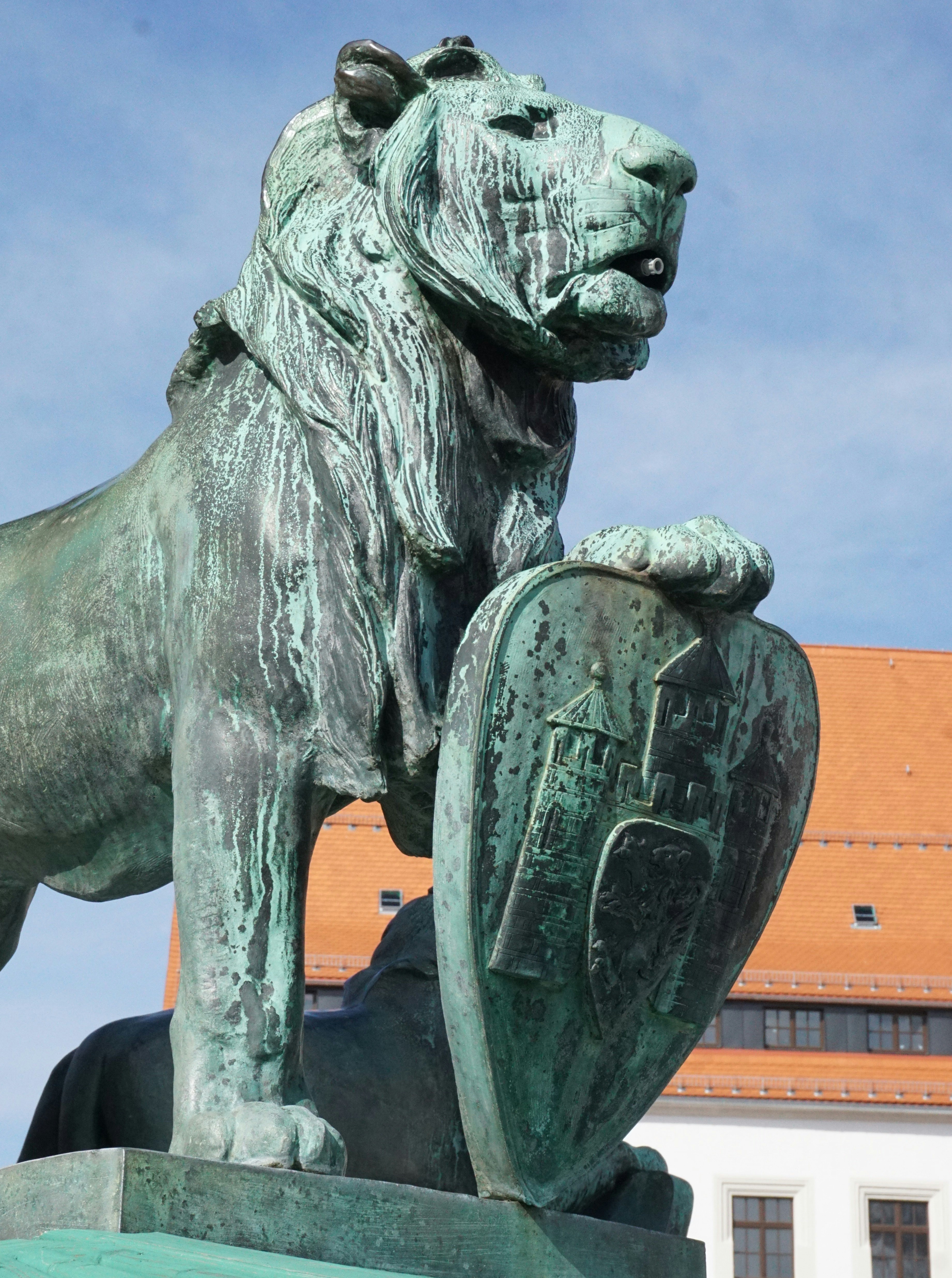 Patina Sentinel: The Bronze Lion with Shield Against a Sunlit Rooftop Backdrop