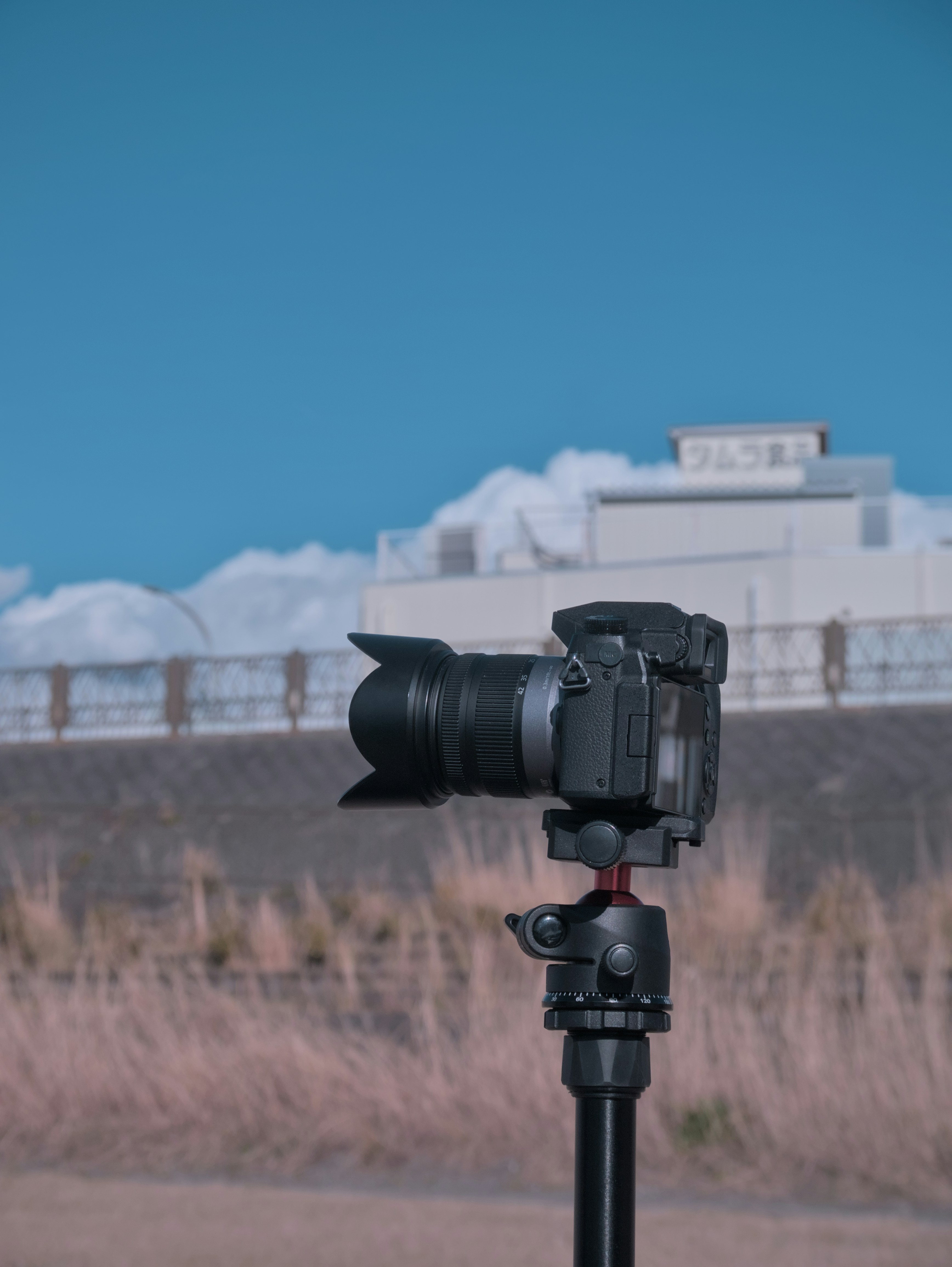 A Panasonic Lumix G6 camera mounted on a tripod, poised against a backdrop of clouds and distant structures.