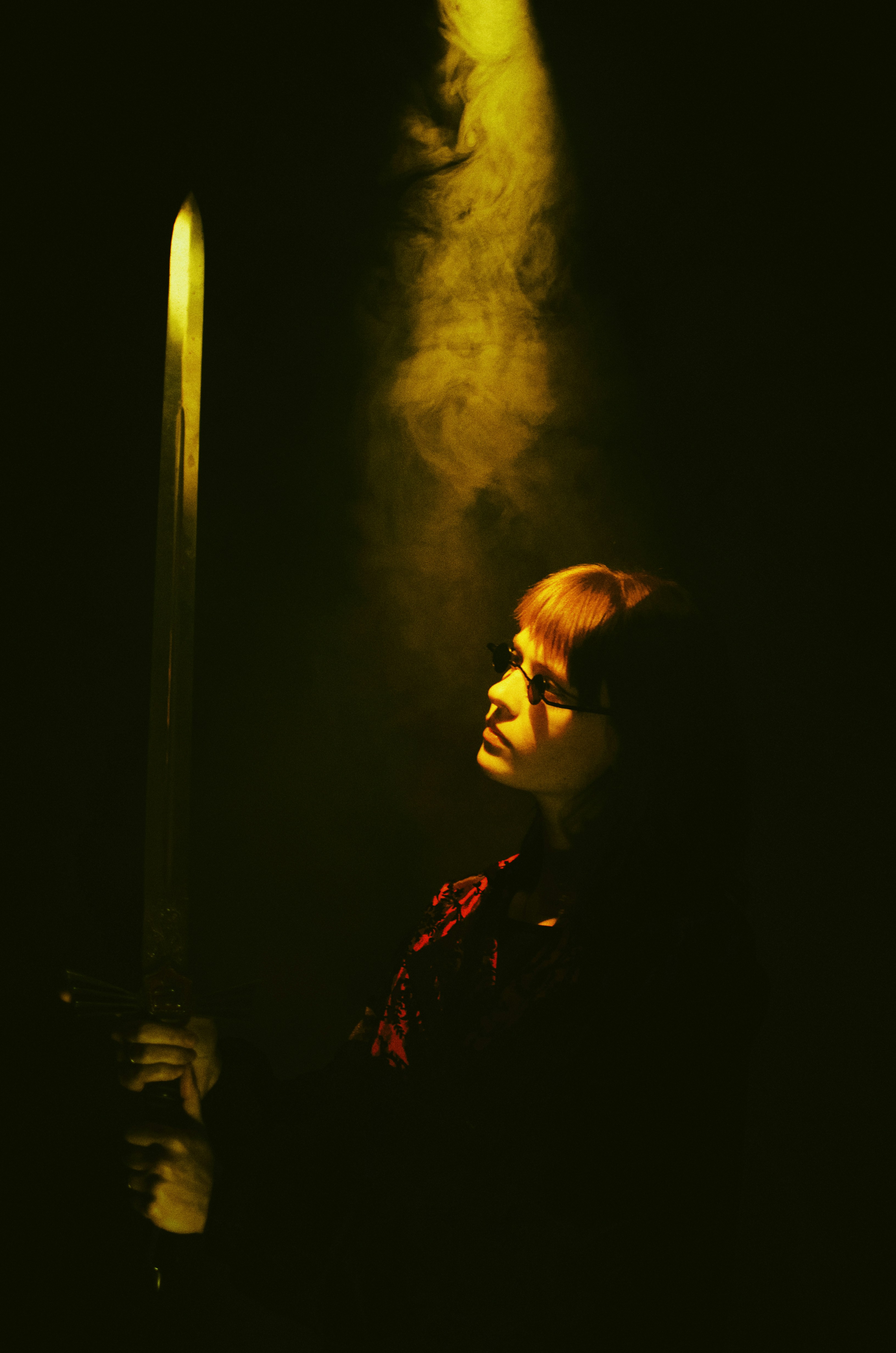 A figure holding a sword stands under a beam of light, surrounded by swirling smoke, creating an aura of mystery and strength.