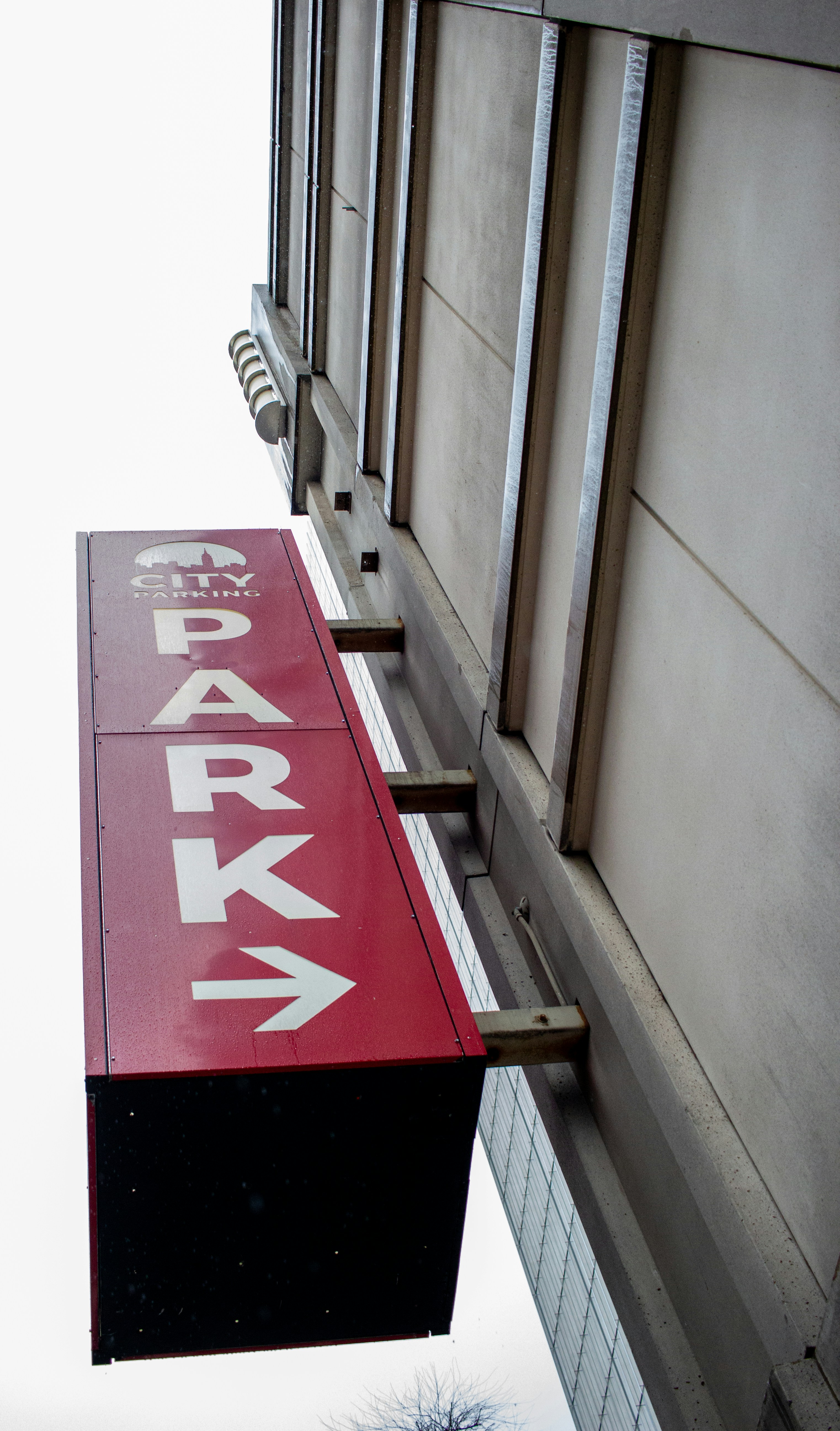 Vertical parking sign against a neutral backdrop, directing drivers to city parking facilities.