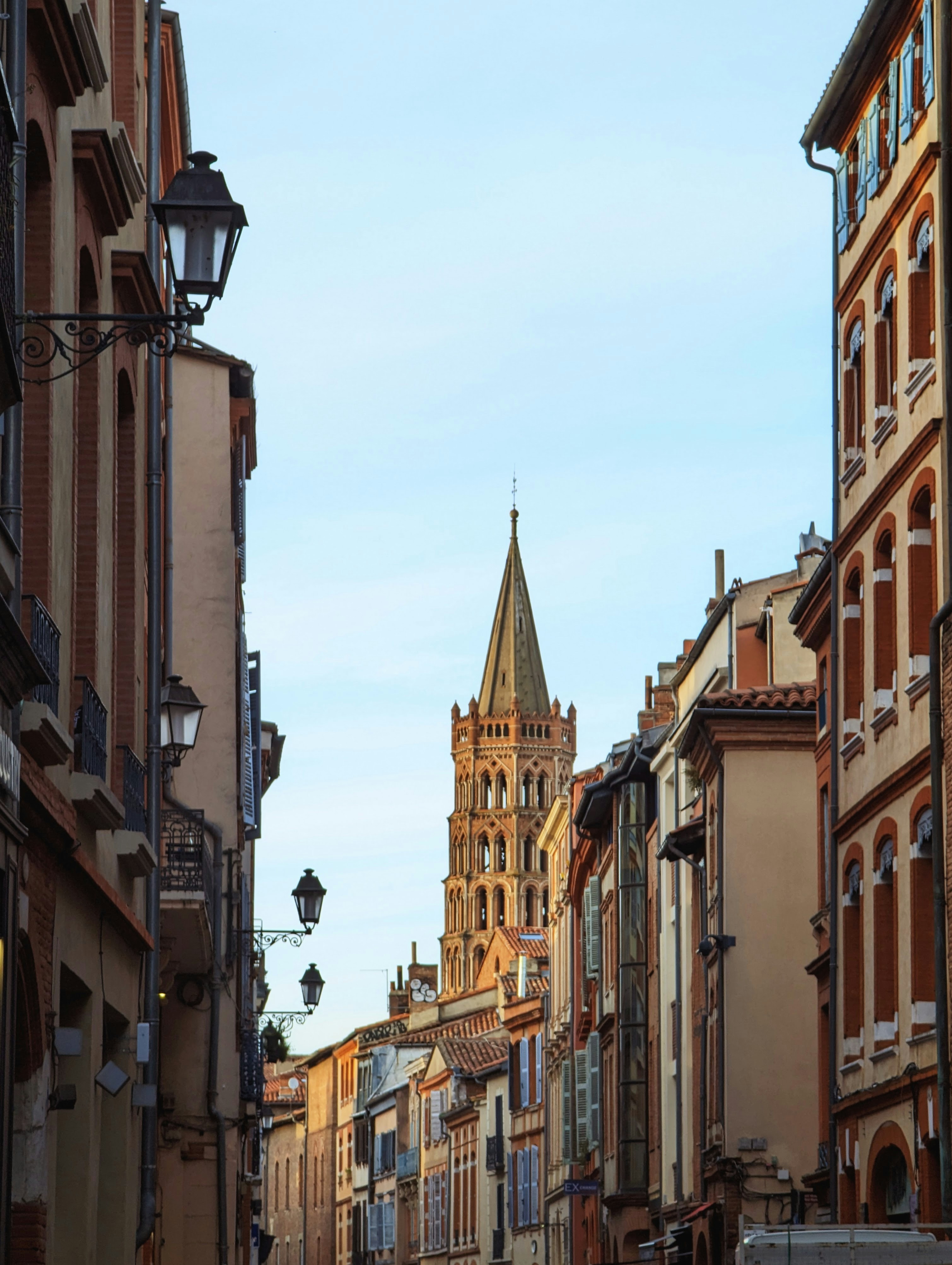 Narrow Toulousian street flanked by historical terracotta buildings, leading the eye toward the striking Basilique Saint-Sernin in the distance