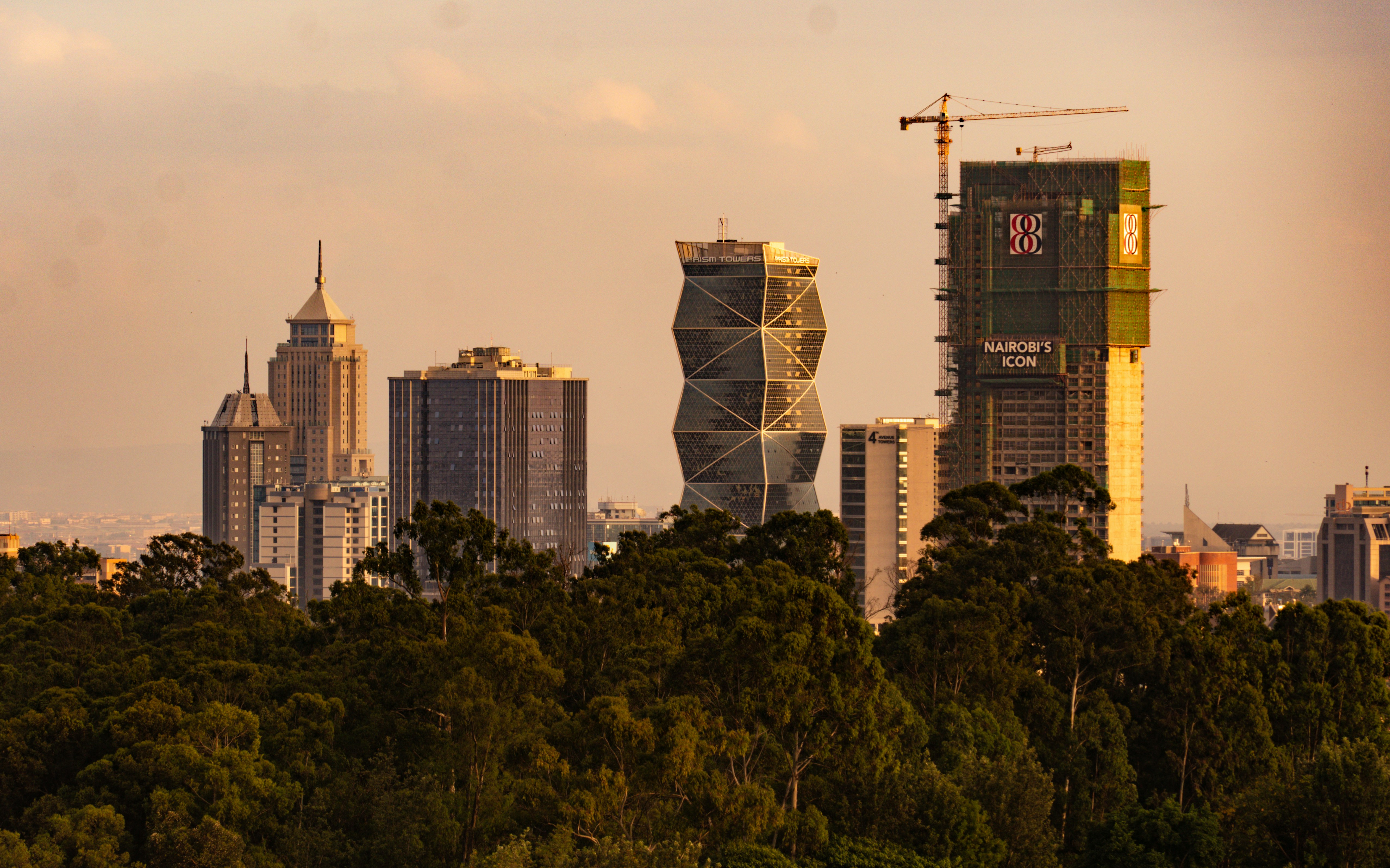 Modern skyscrapers rise above lush greenery, showcasing a blend of nature and urban development. The scene captures the essence of a vibrant cityscape at dusk.