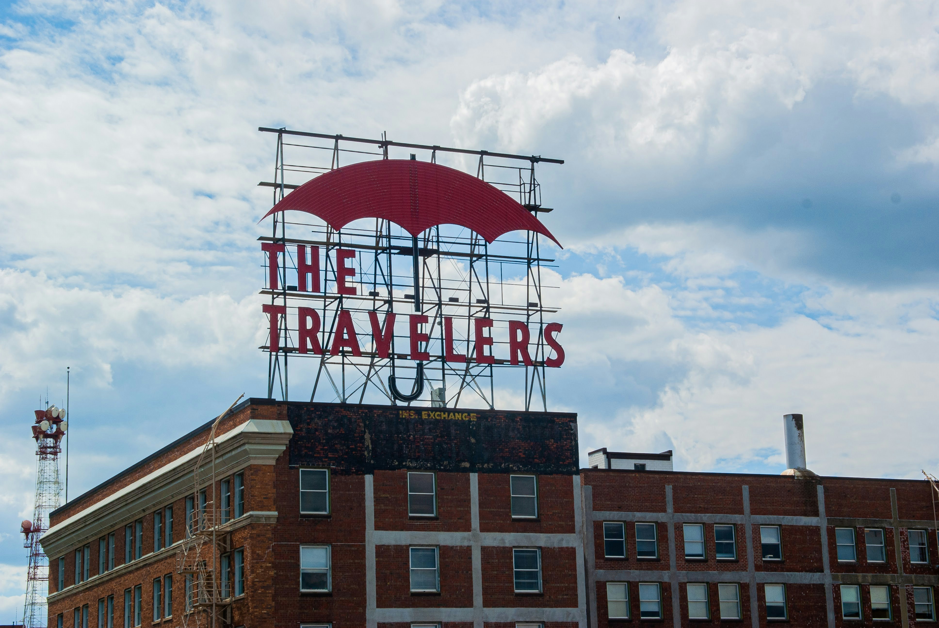 A vintage sign featuring an umbrella and the word 'THE TRAVELERS' prominently displayed on a building rooftop against a cloudy sky.
