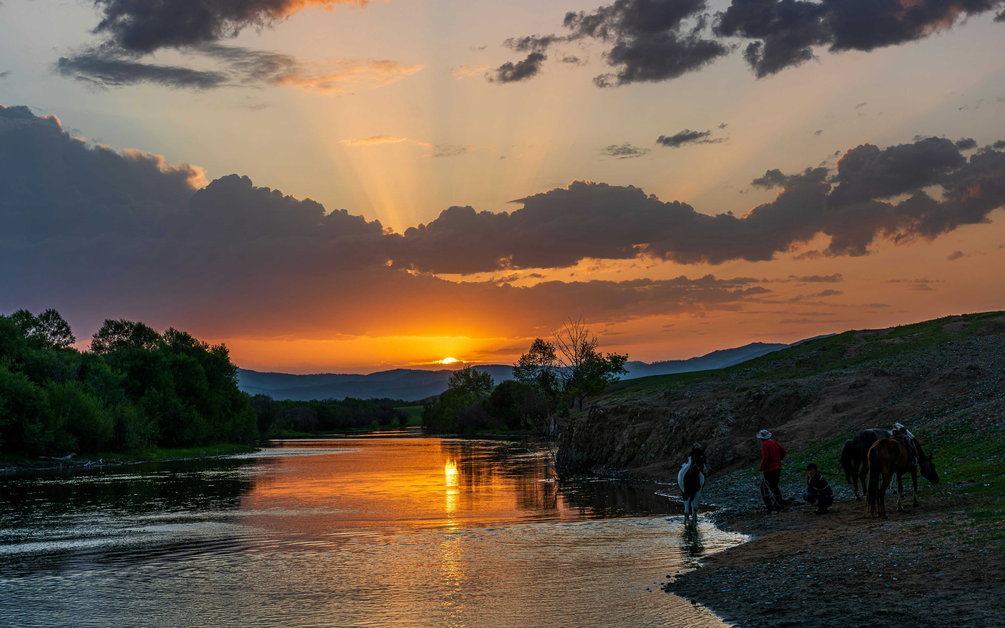 Sunset casting golden hues over the Onon River as silhouettes of people and horses line the shore.