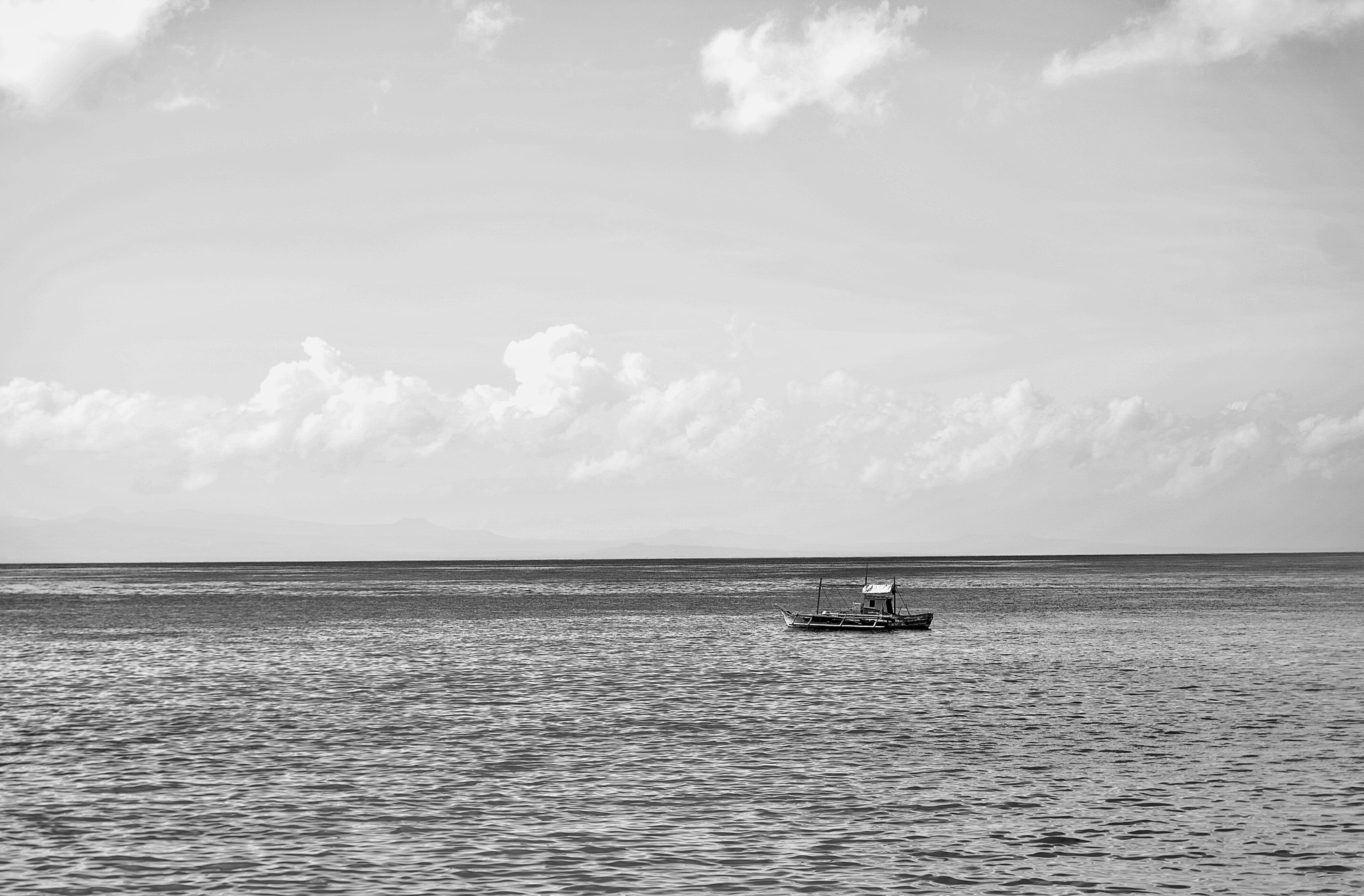 Small boat floating on expansive sea under a partly cloudy sky.