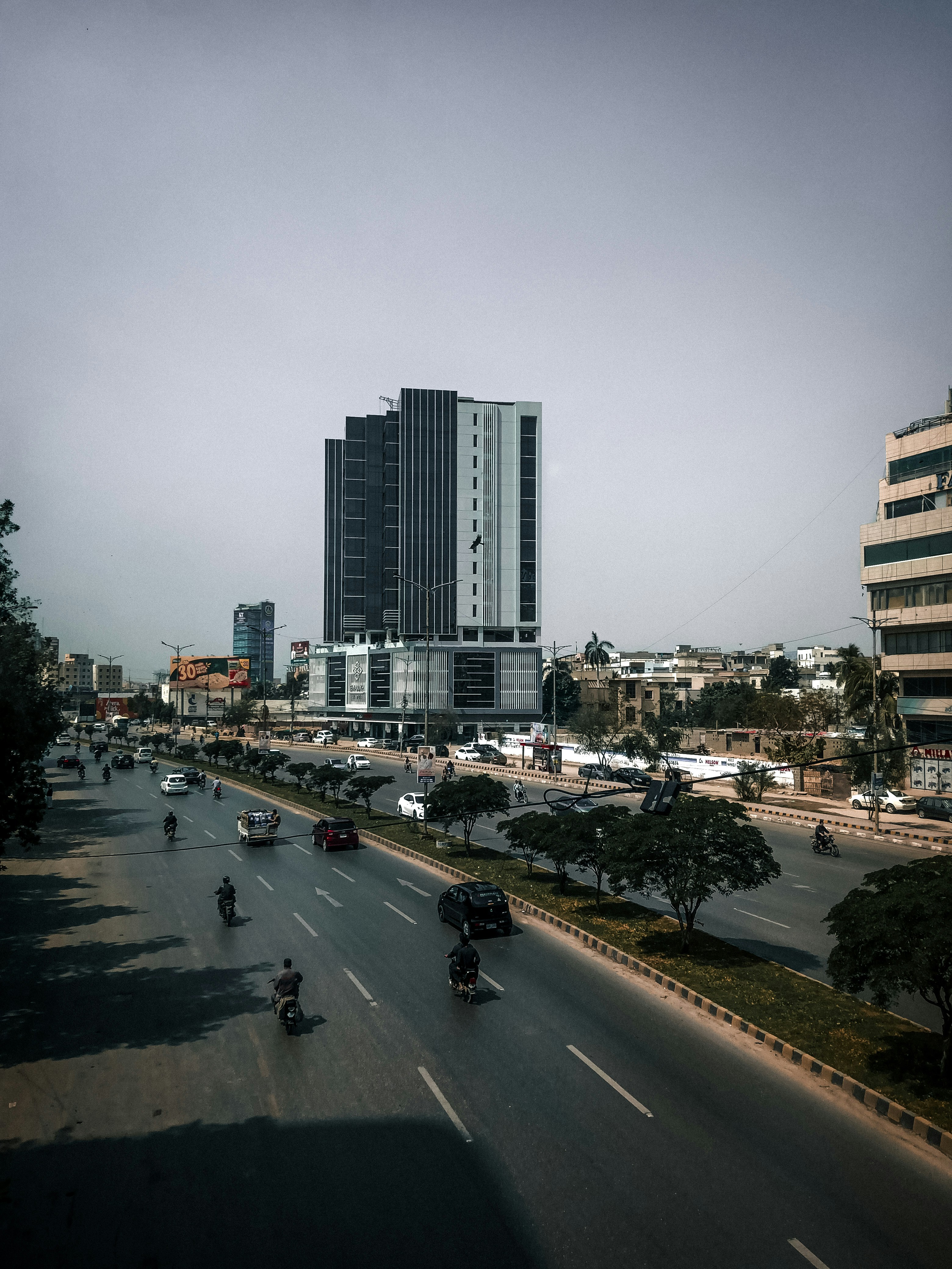 High-rise building stands prominently against a clear sky, surrounded by bustling traffic and urban greenery.