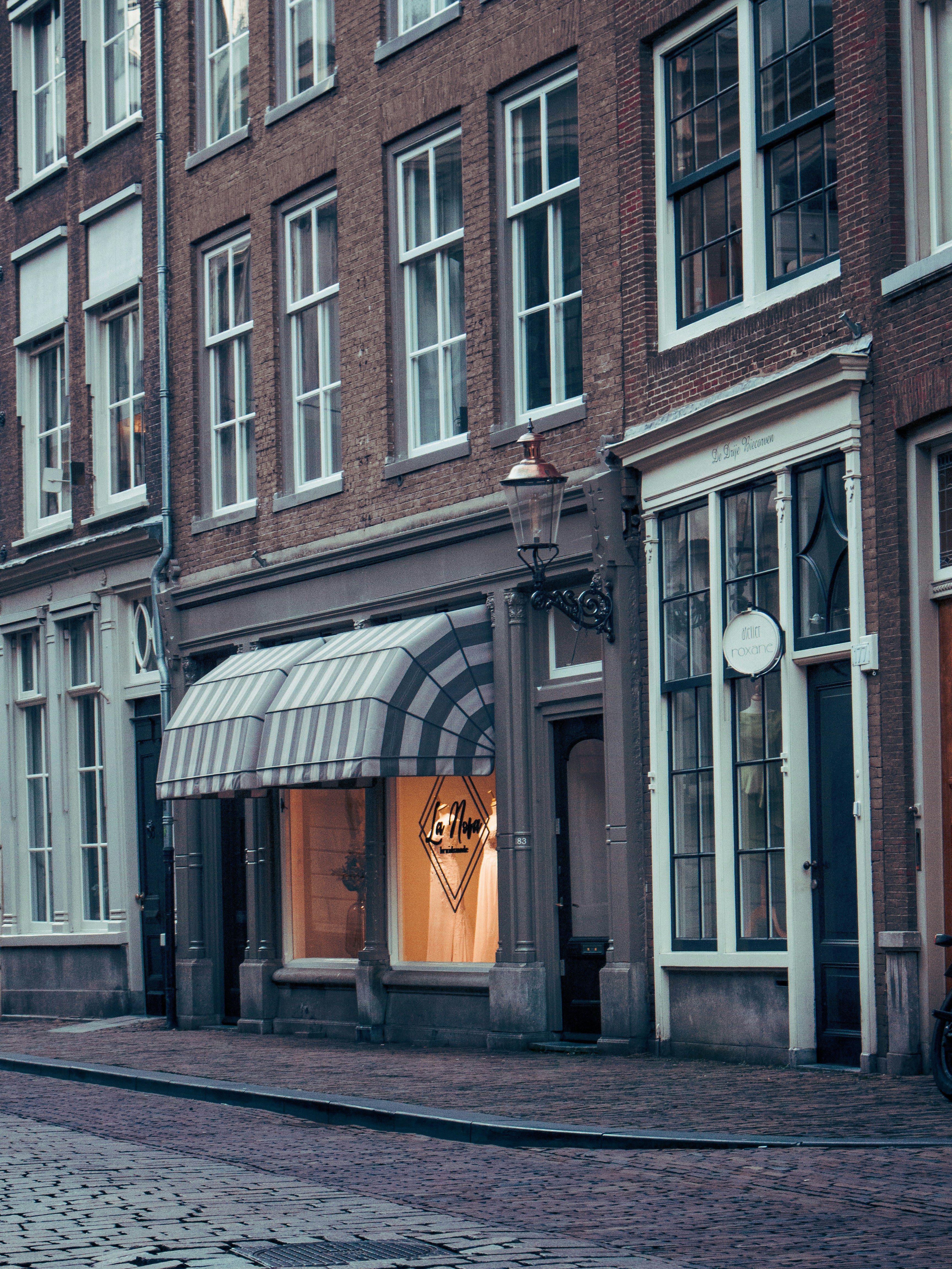 Amber Window Under the Striped Canopy: Quiet European Streetfront at Dusk