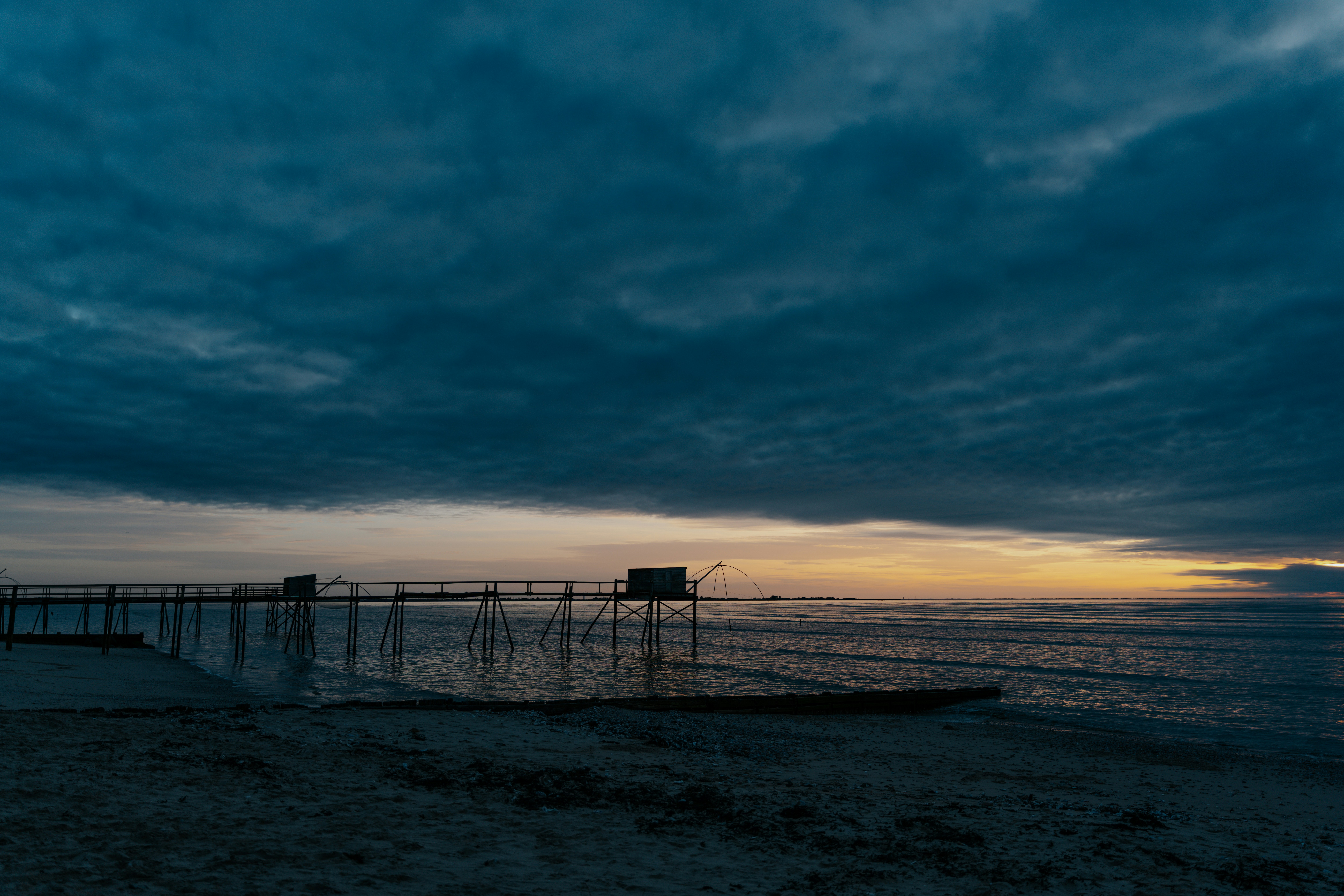Une jetée assise au sommet d’une plage de sable sous un ciel nuageux ...