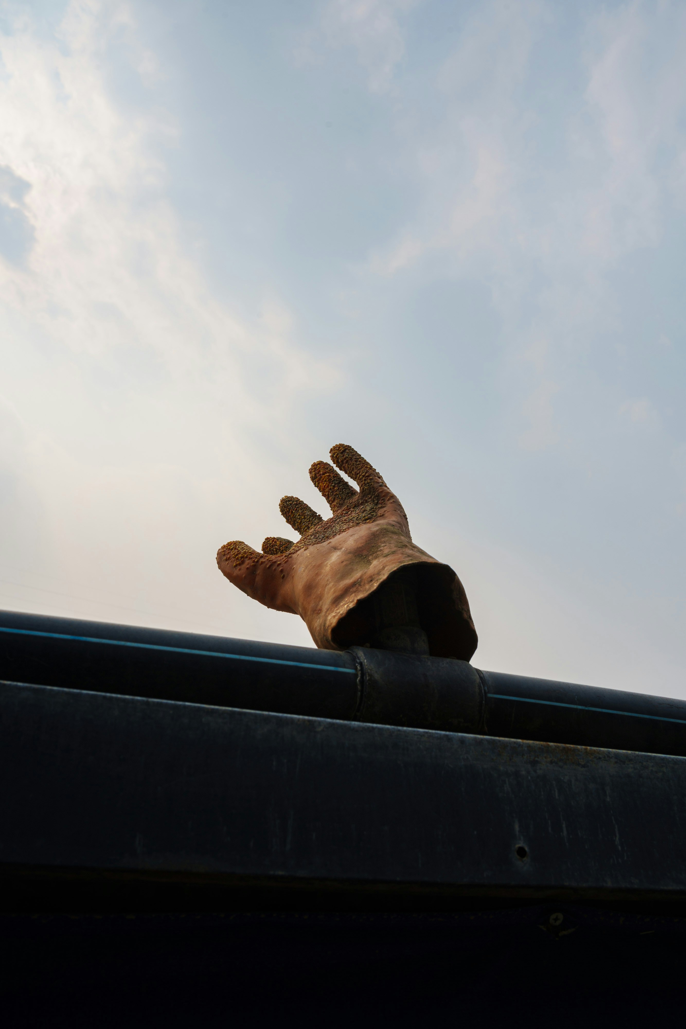 A Gloved Hand Emerges from the Rooftop Edge Against a Pale Sky