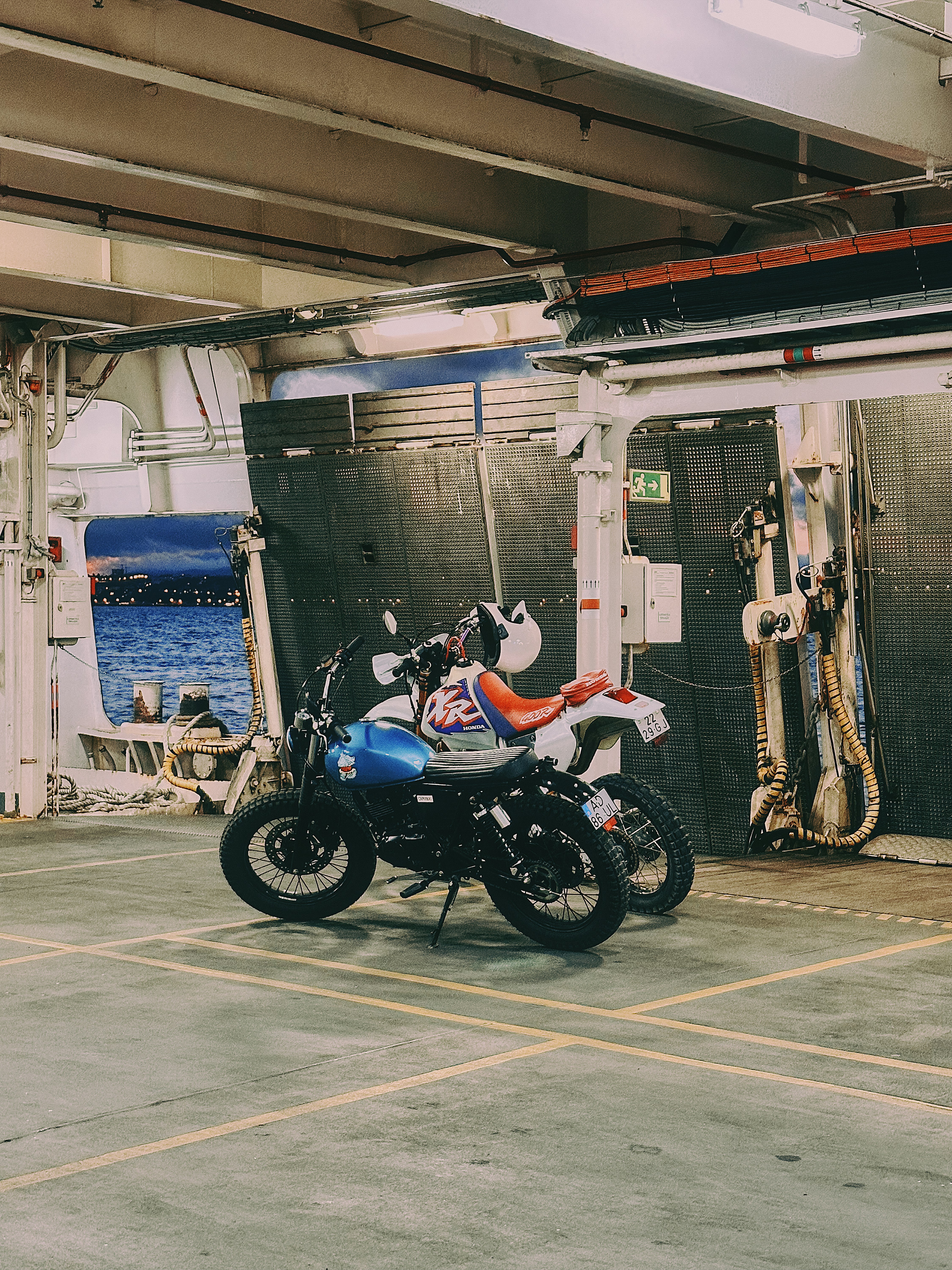 Blue-and-White Dual-Sport Resting on a Ferry Deck Beneath Warm Industrial Lighting