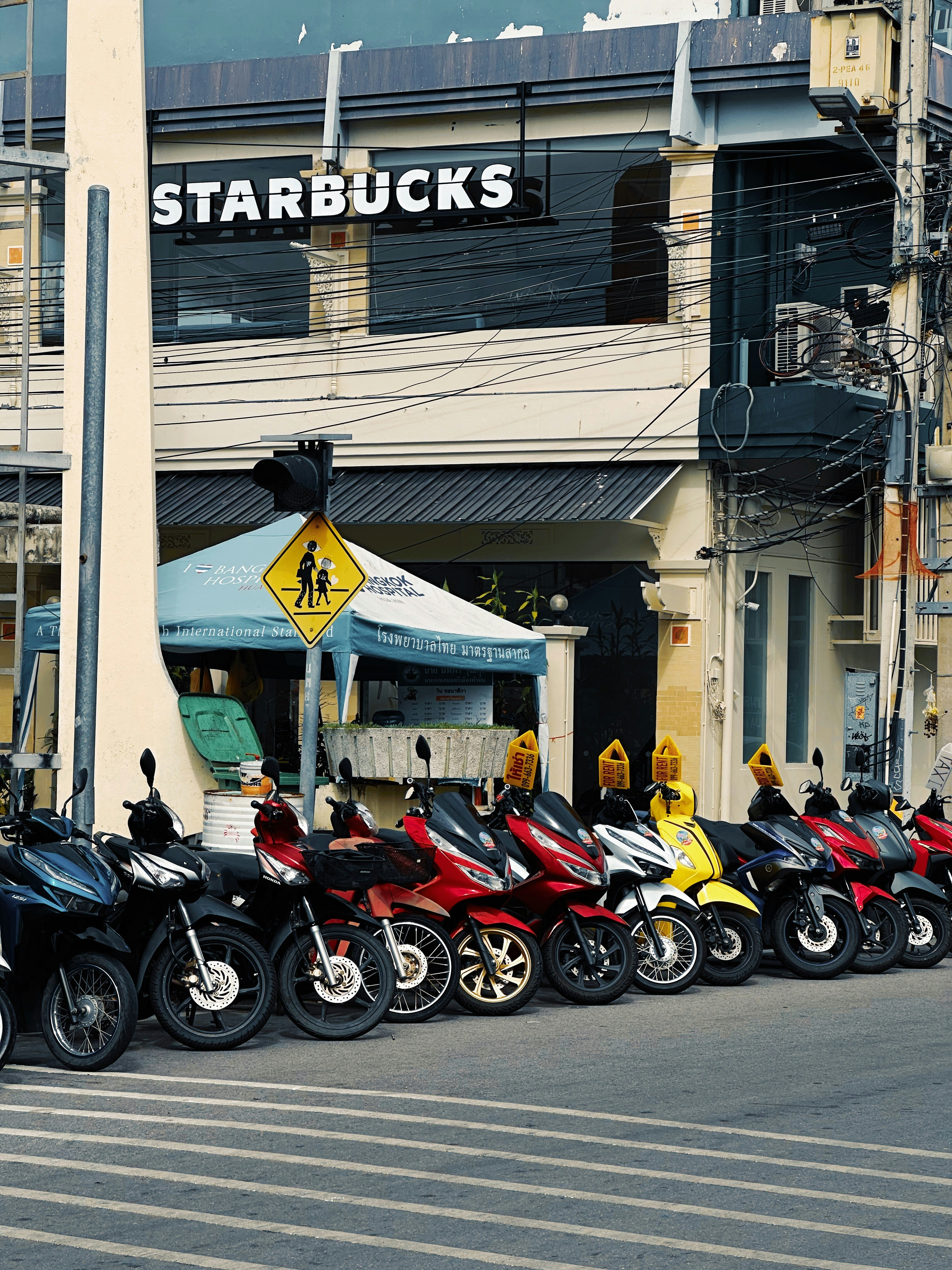 Starbucks Sign Over a Parade of Motorbikes on a Wired City Street