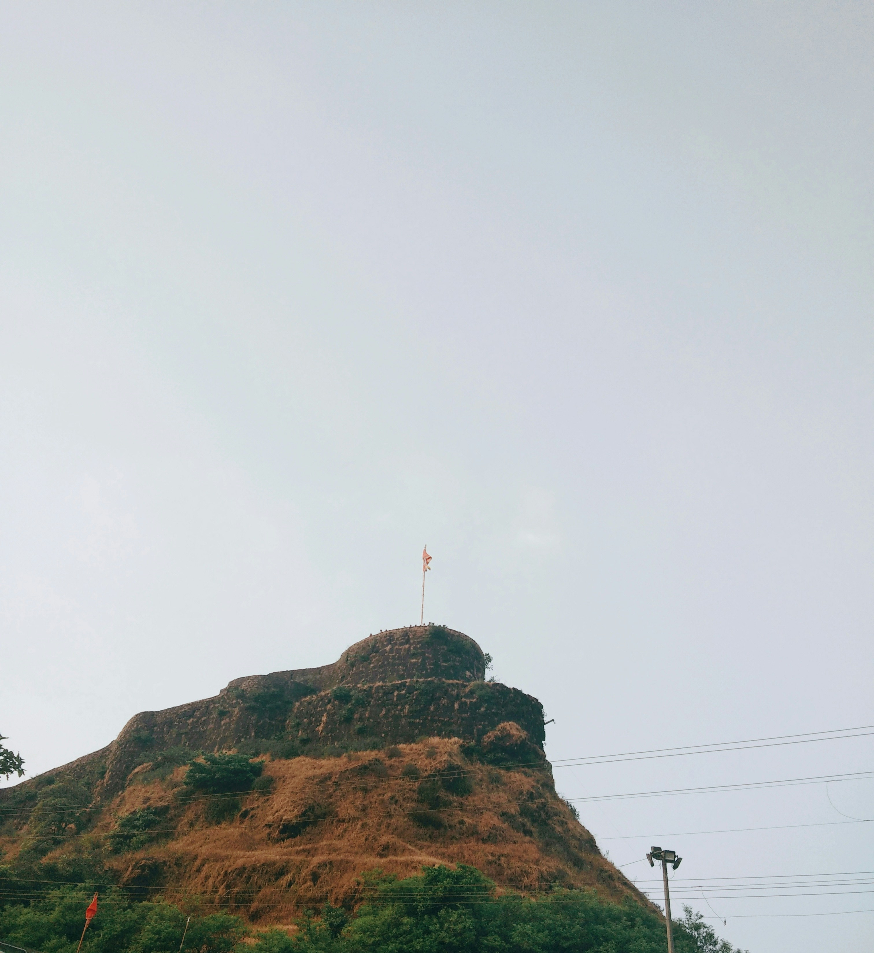 Terraced hillside with a flag on a small summit under a pale sky, capturing the quiet elevation and distant power lines.