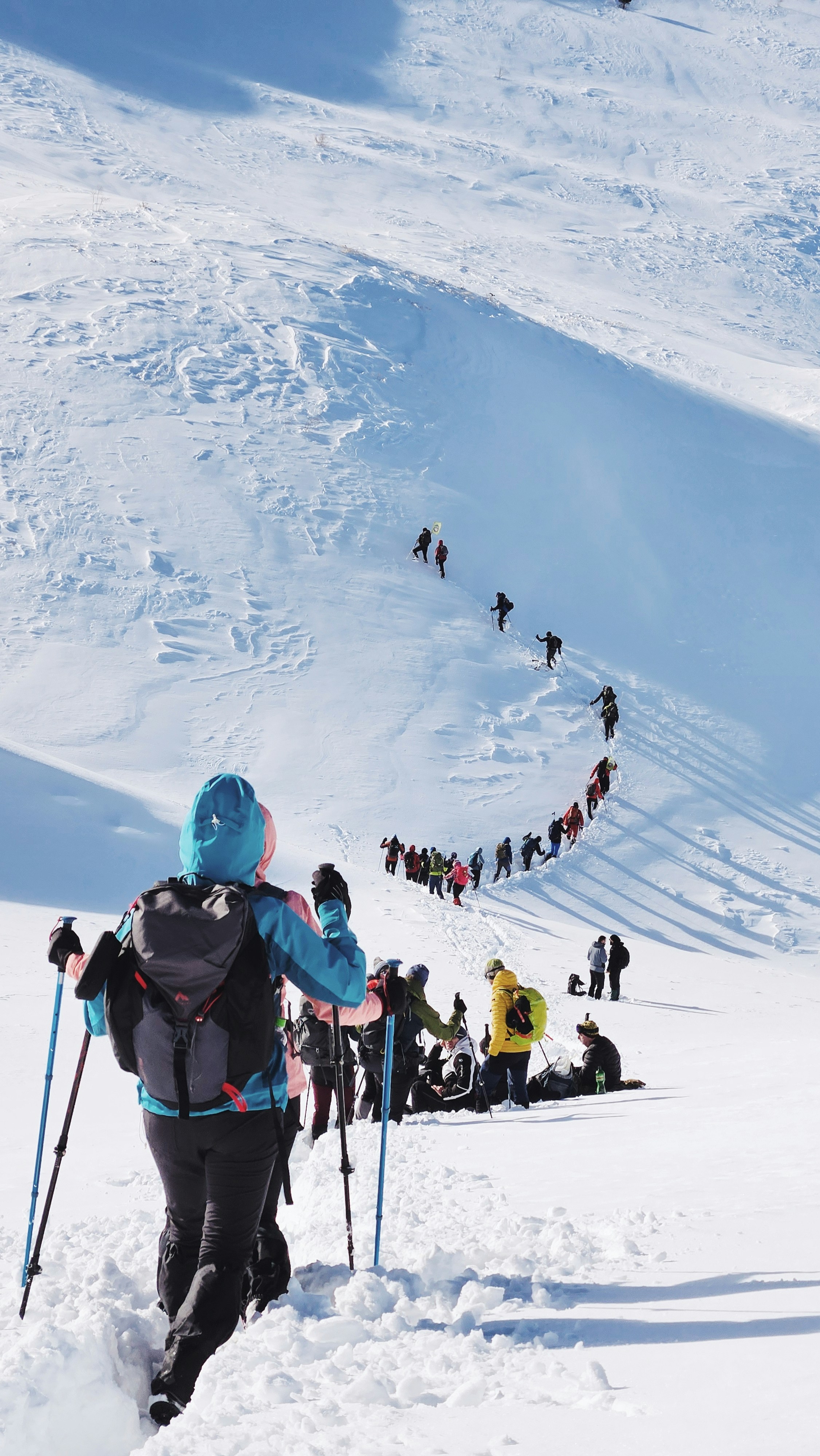 A group of people walking up the side of a snow covered slope photo ...