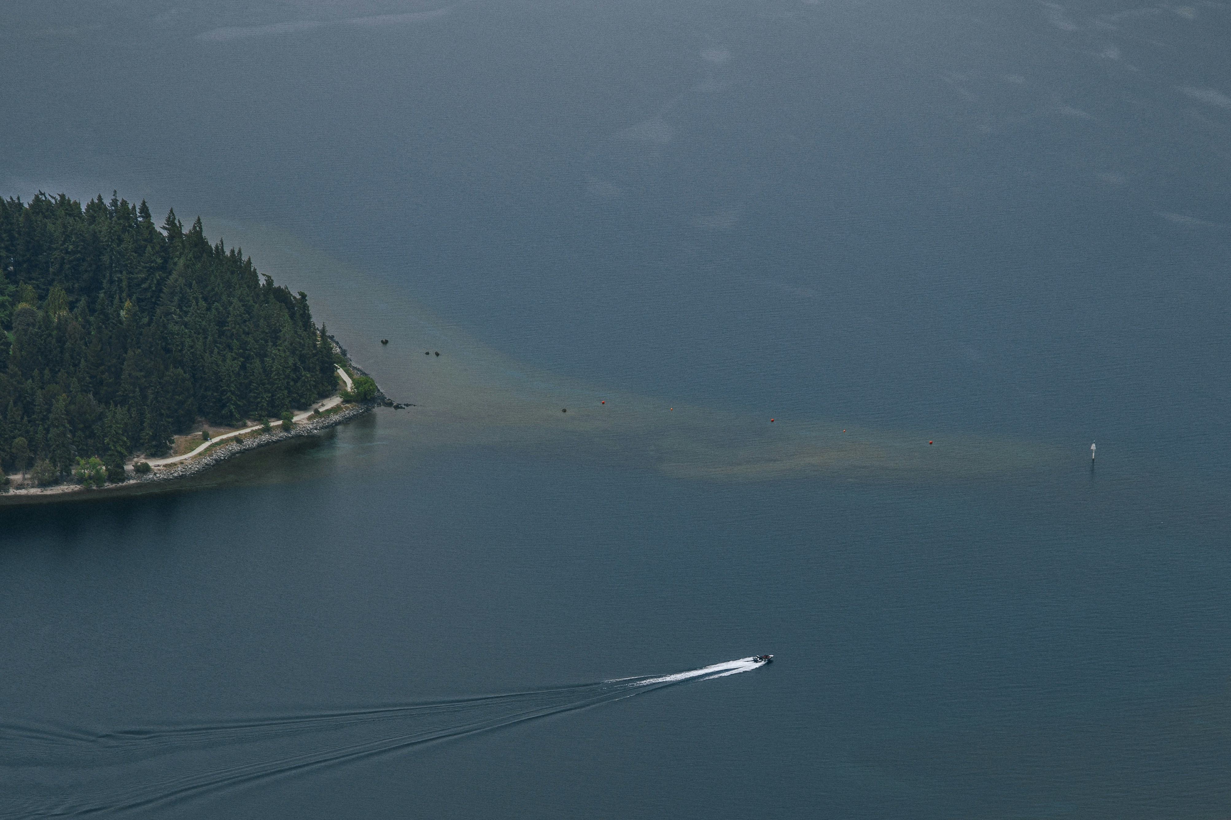 Small island with dense forest surrounded by calm blue waters, a speedboat creating a wake as it glides across the surface.