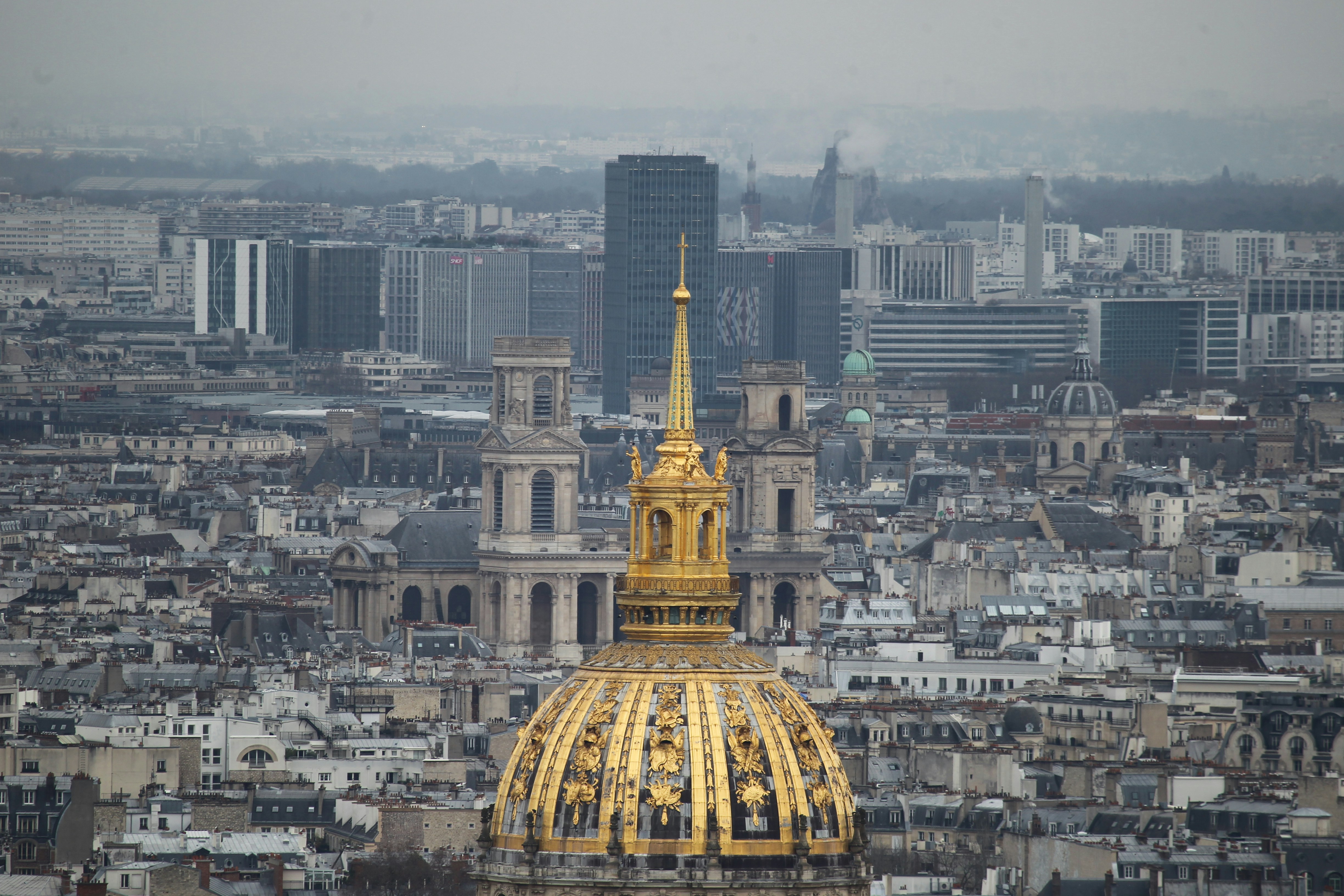 Golden dome of a historic building stands out against a sprawling cityscape under a cloudy sky.