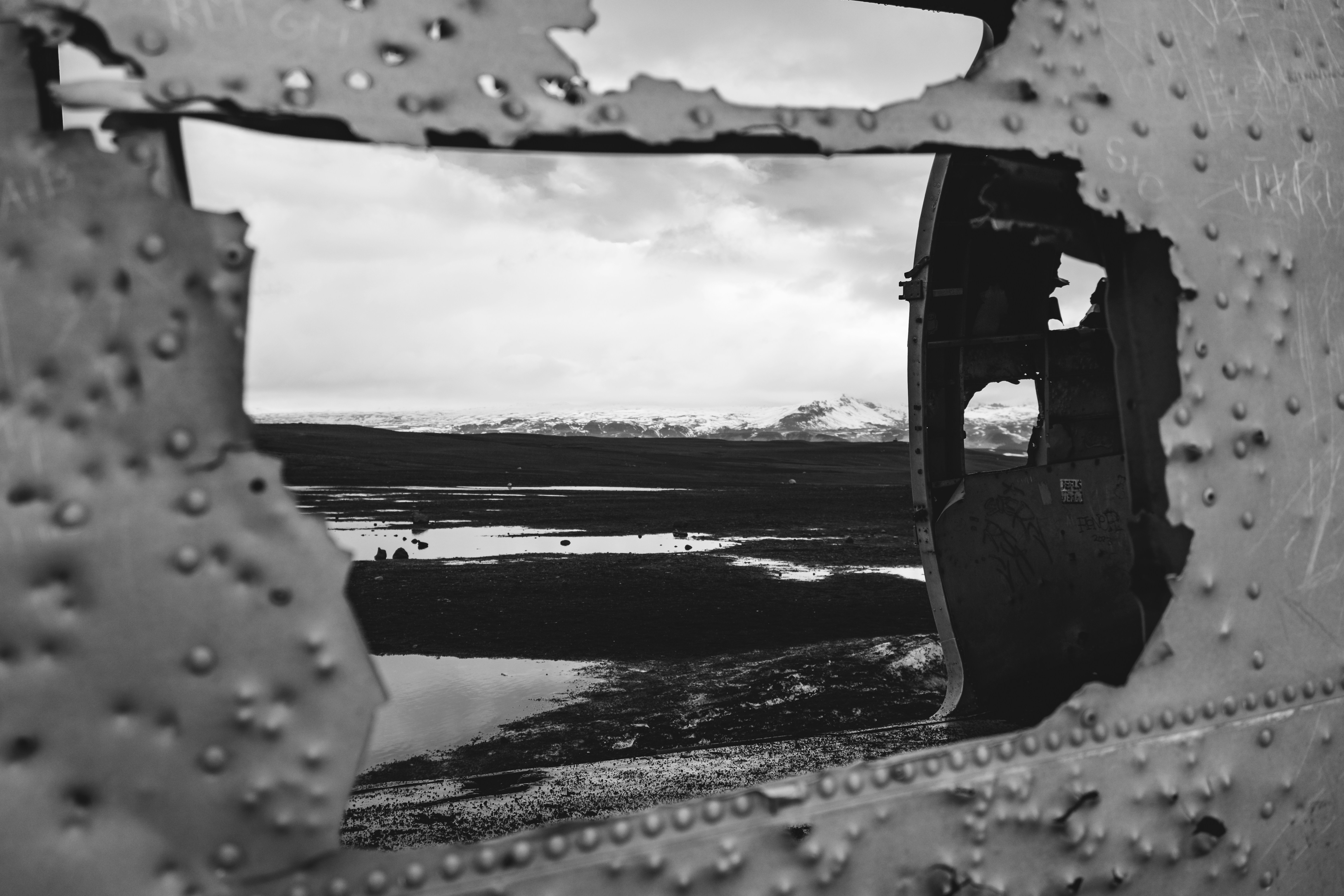 Fragmented Skyline: A Tank Hull Framed by a Pocked Metal Window