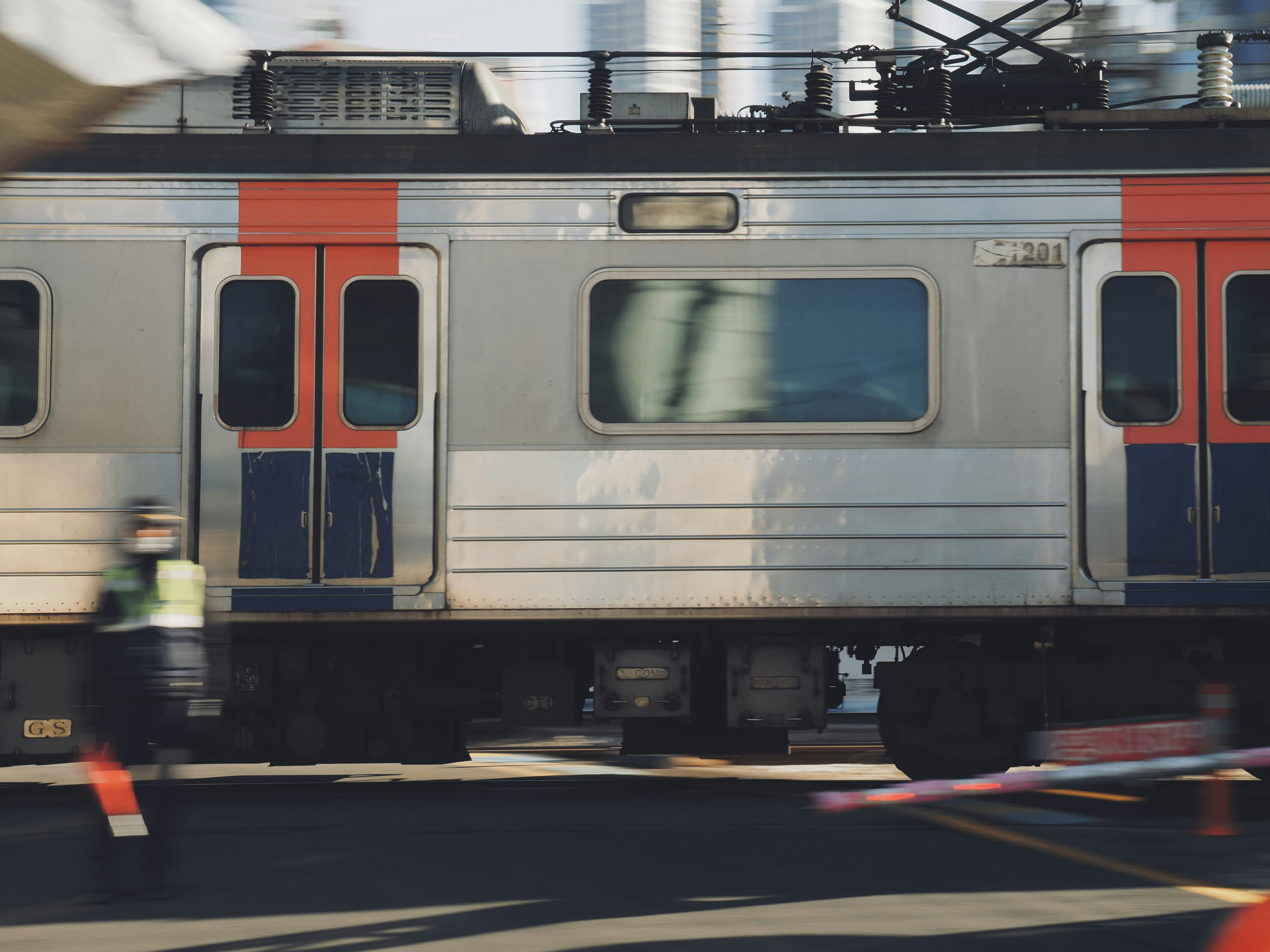 A silver train traveling down train tracks next to a tall building ...