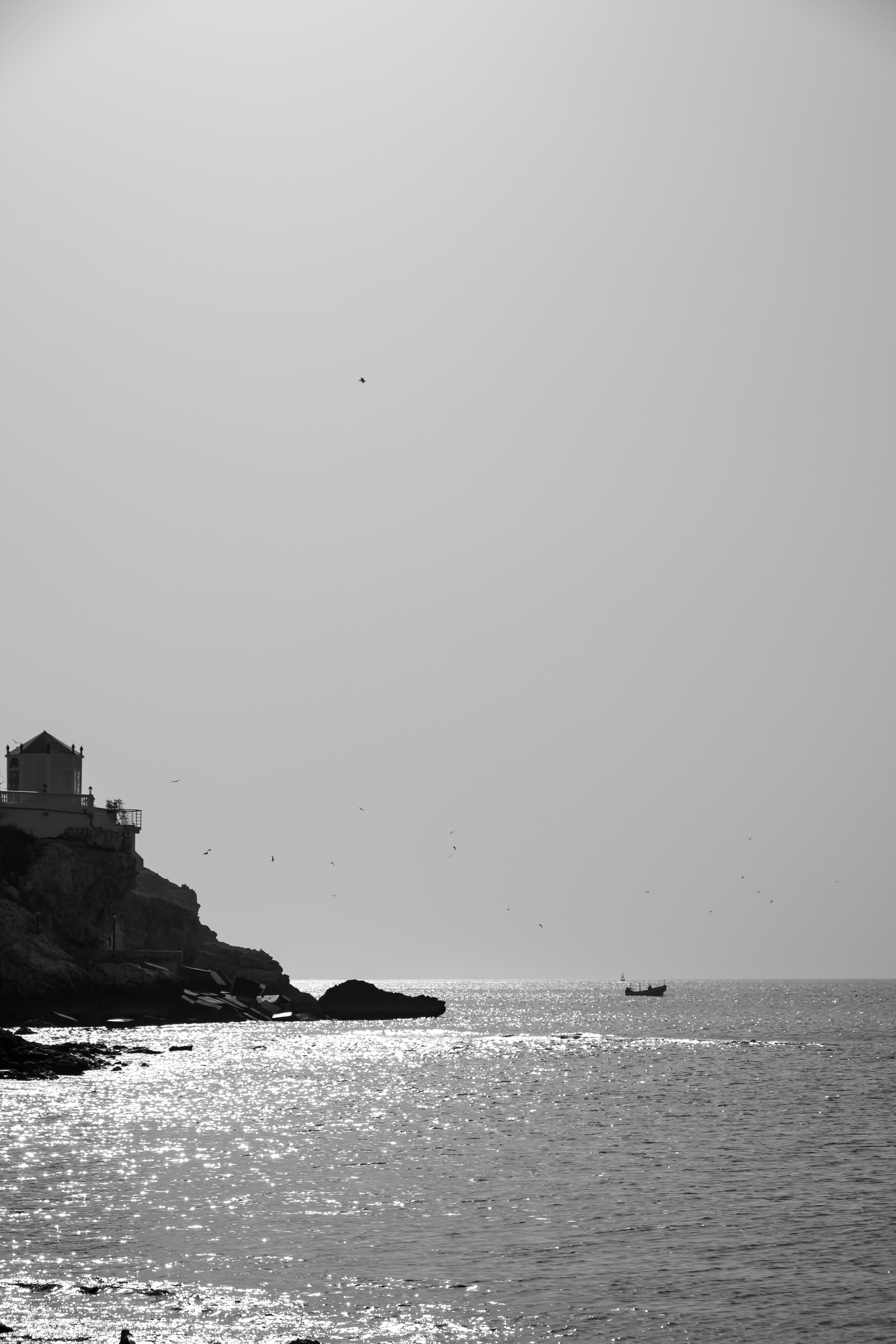 Cliffside Outpost and a Lone Boat Over a Glimmering Sea