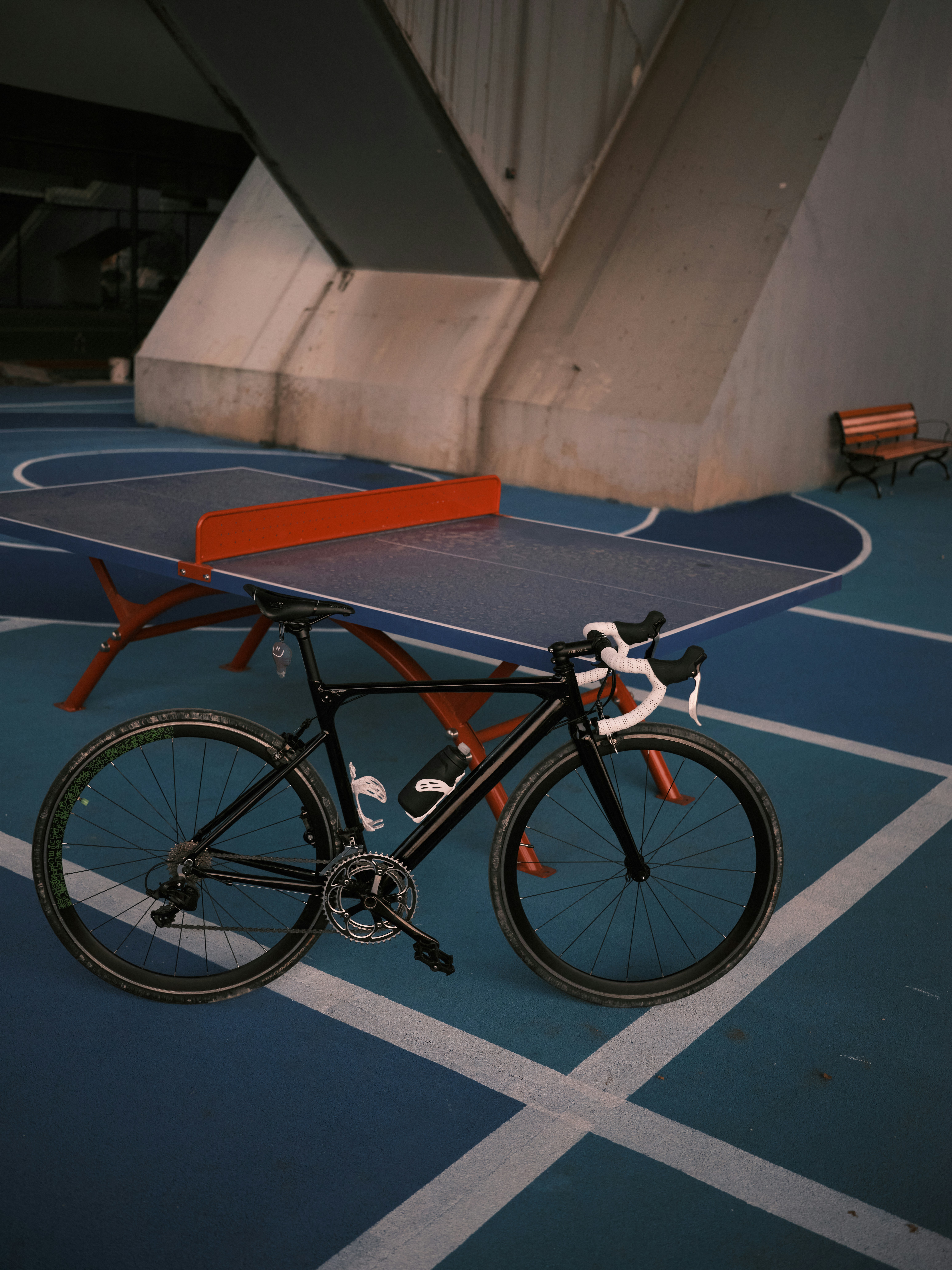 Black road bike rests beside a blue tennis court with an orange table tennis net