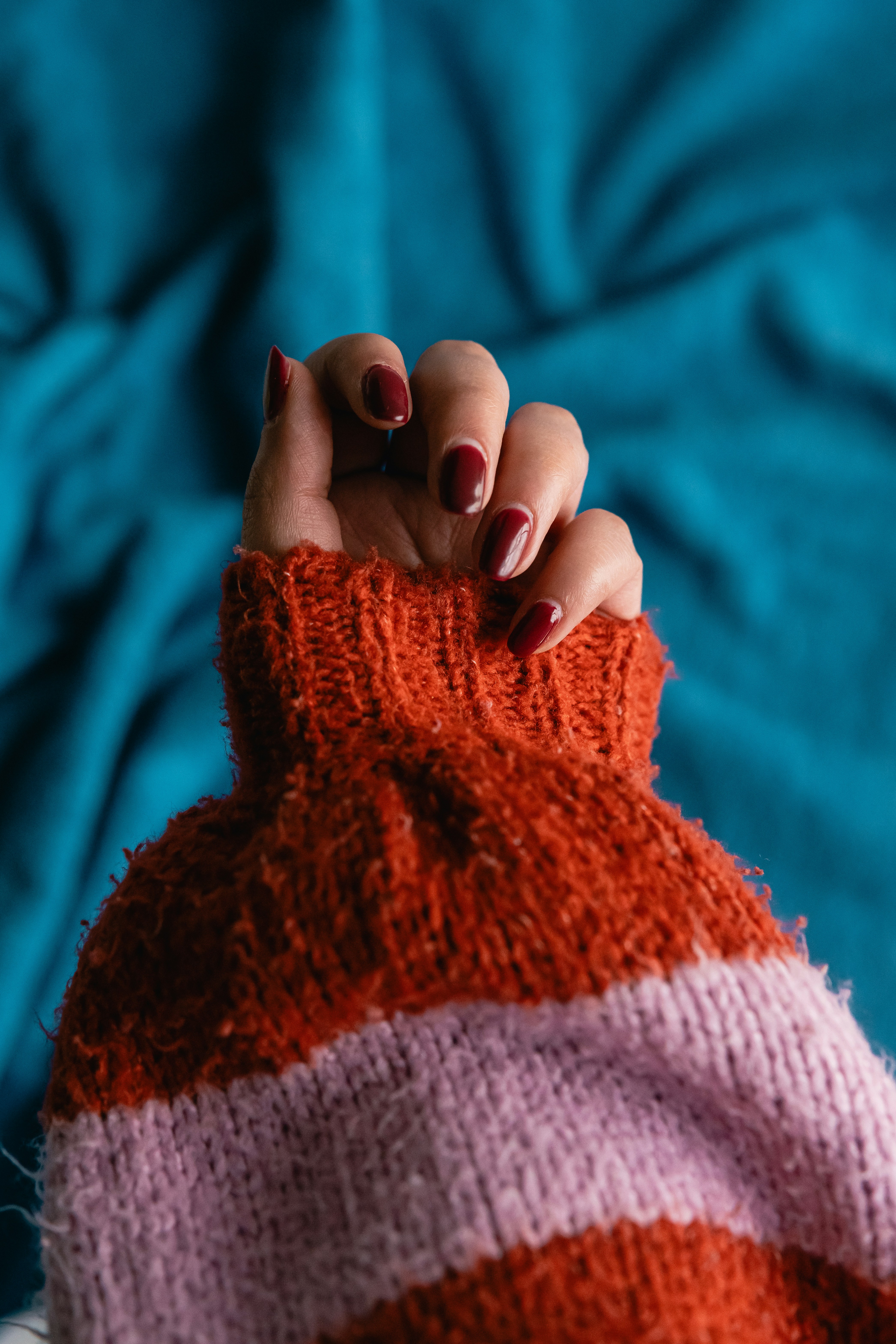 Crimson Grasp Against Azure Backdrop: A Close-Up of Knit Texture and Painted Nails
