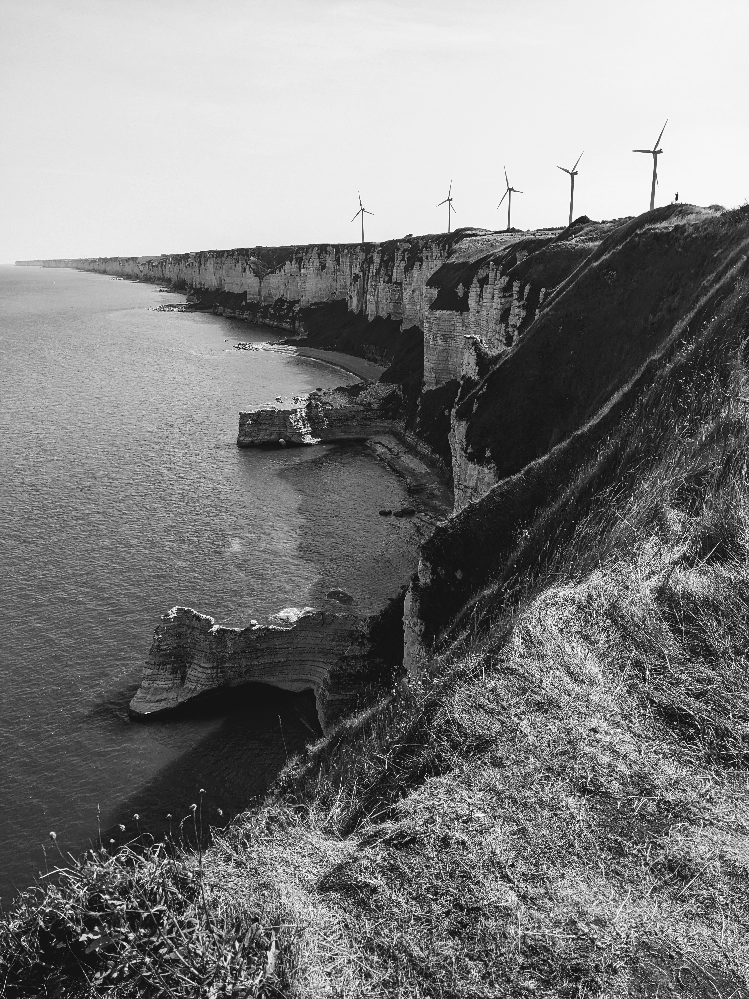 A black and white photo of a cliff with wind mills in the background ...