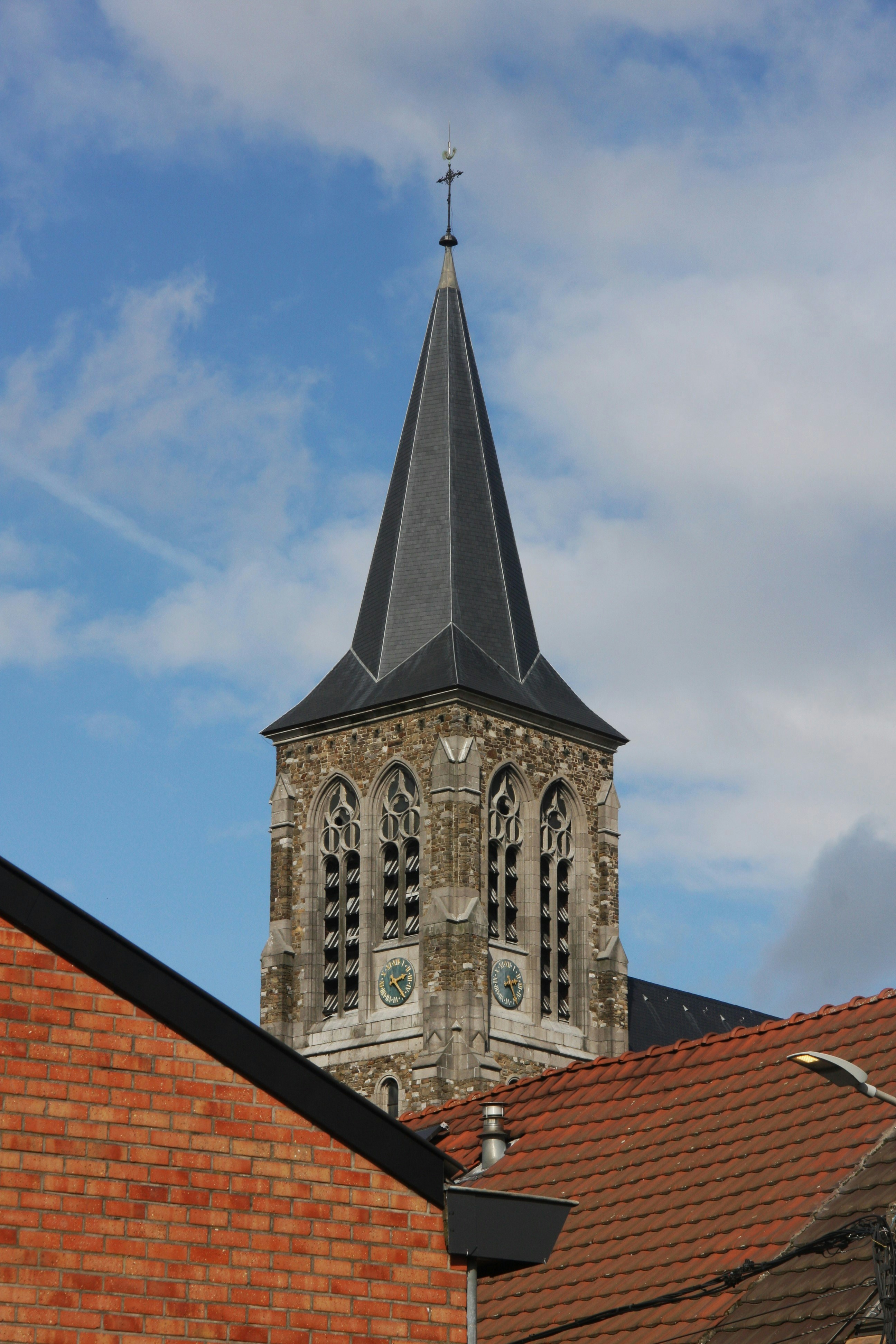 Vue d'une église, sous un ciel bleu, avec deux maisons en avant-plan.