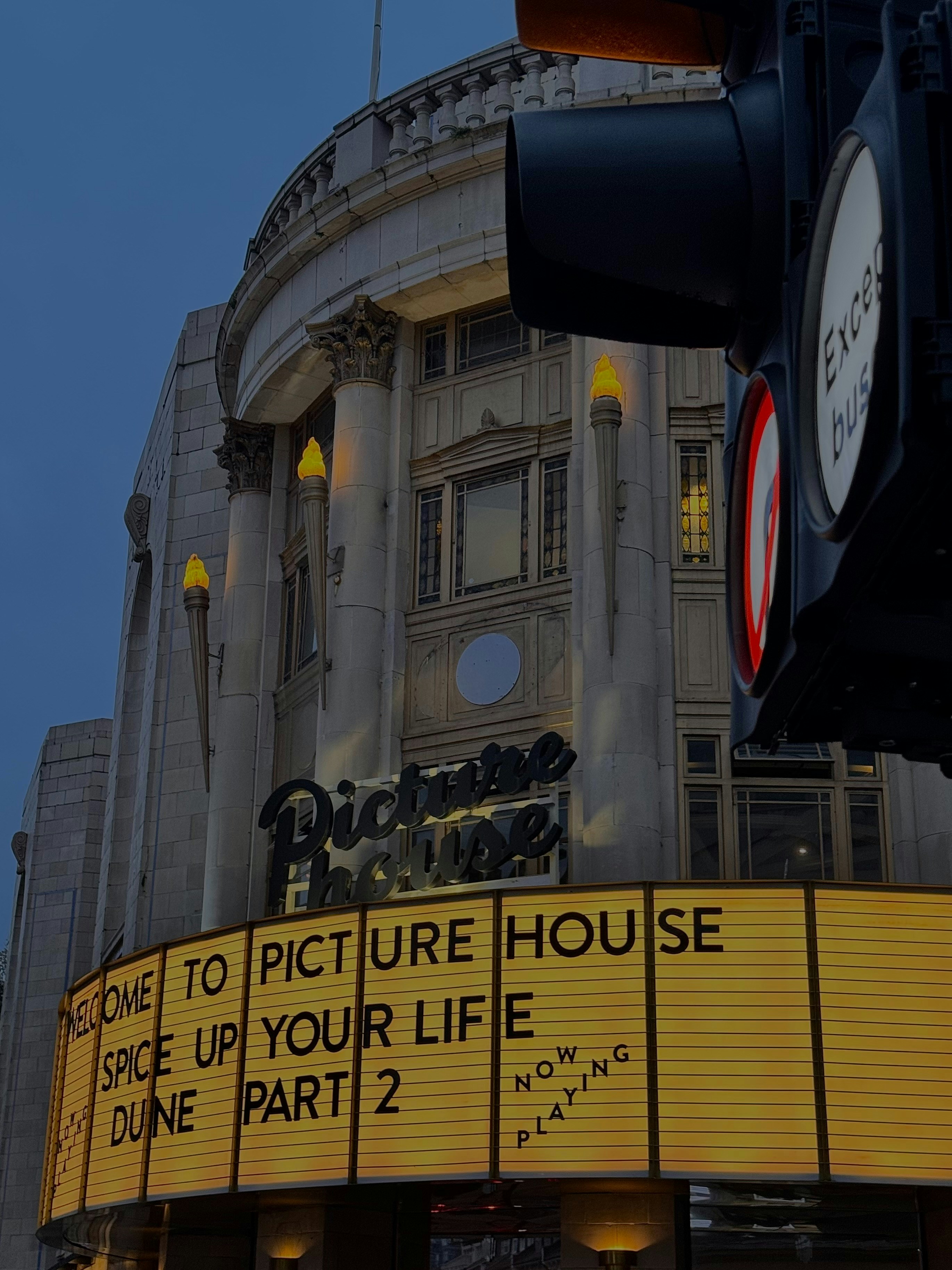 Neon marquee of a vintage cinema framing a street-side sign at dusk