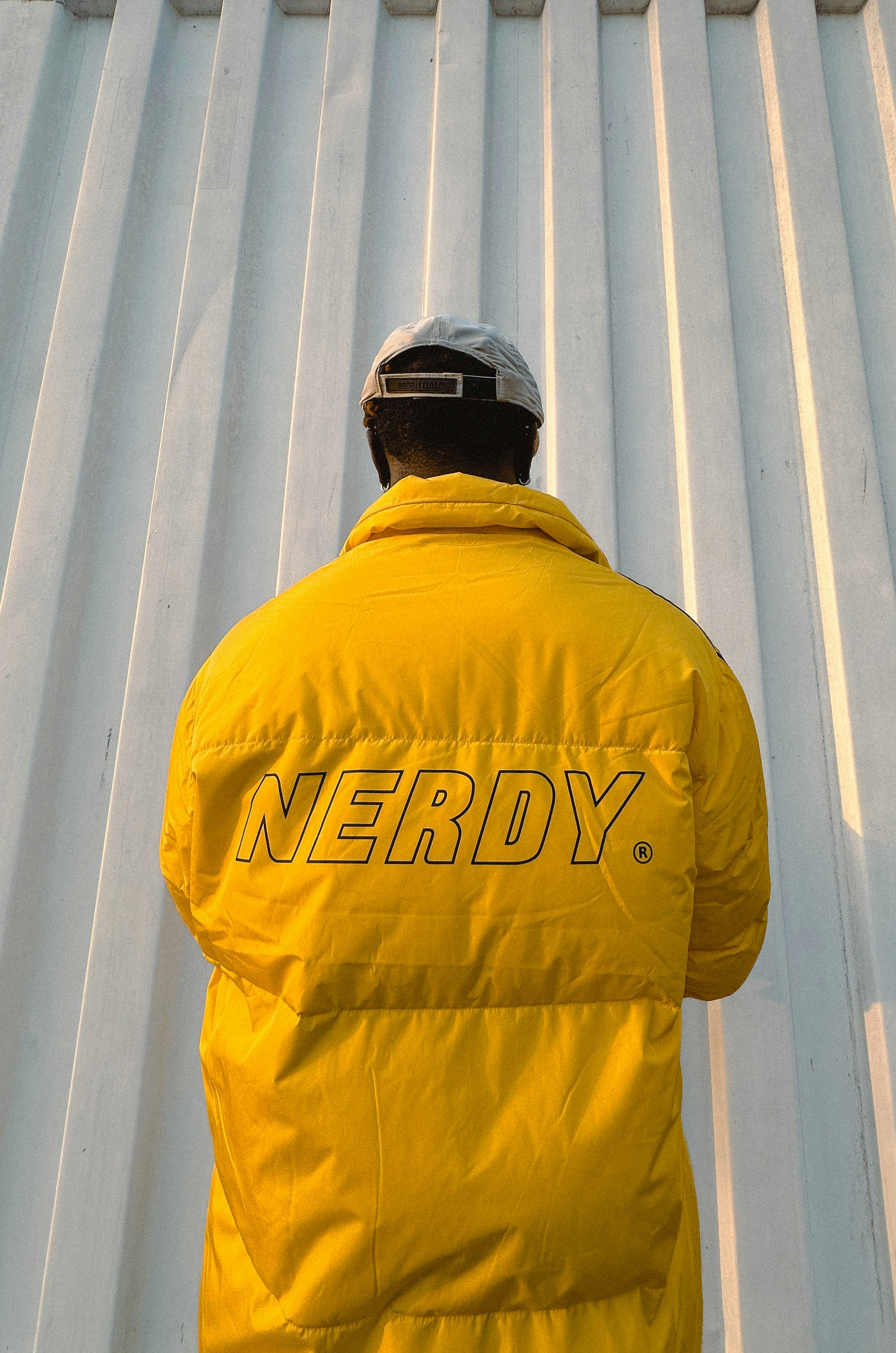 Nerdy in Neon: A Bright Jacket Against a Pale Corrugated Wall
