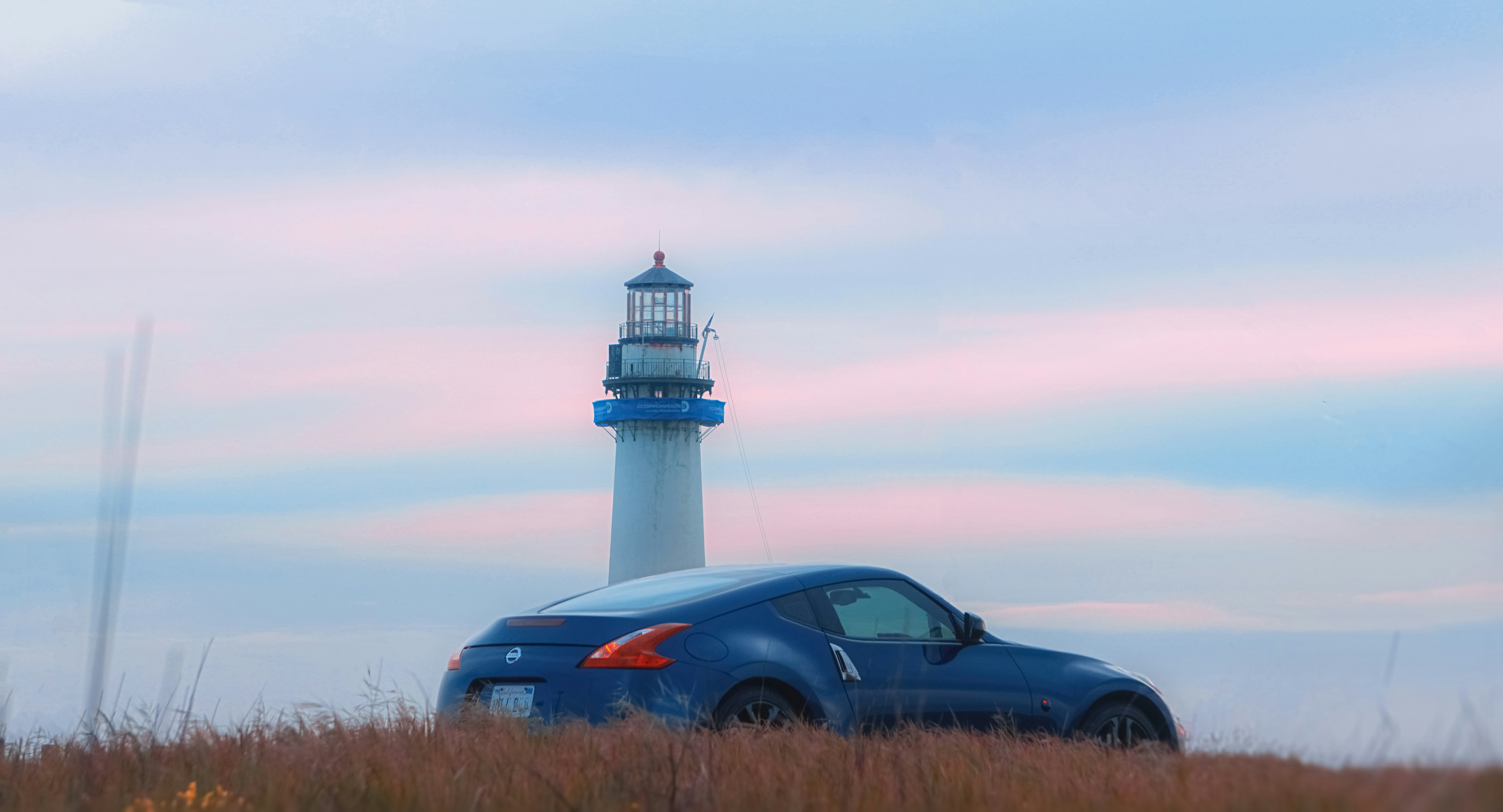 Blue coupe resting near a lighthouse at blue-hour harbor