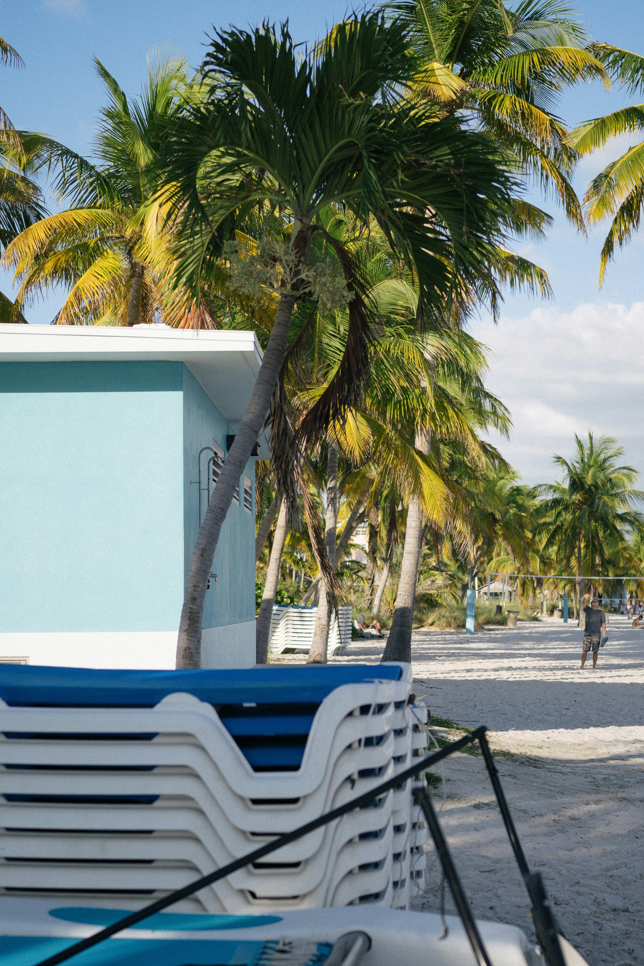 A stack of blue and white striped beach chairs awaits visitors on a sandy beach lined with palm trees.