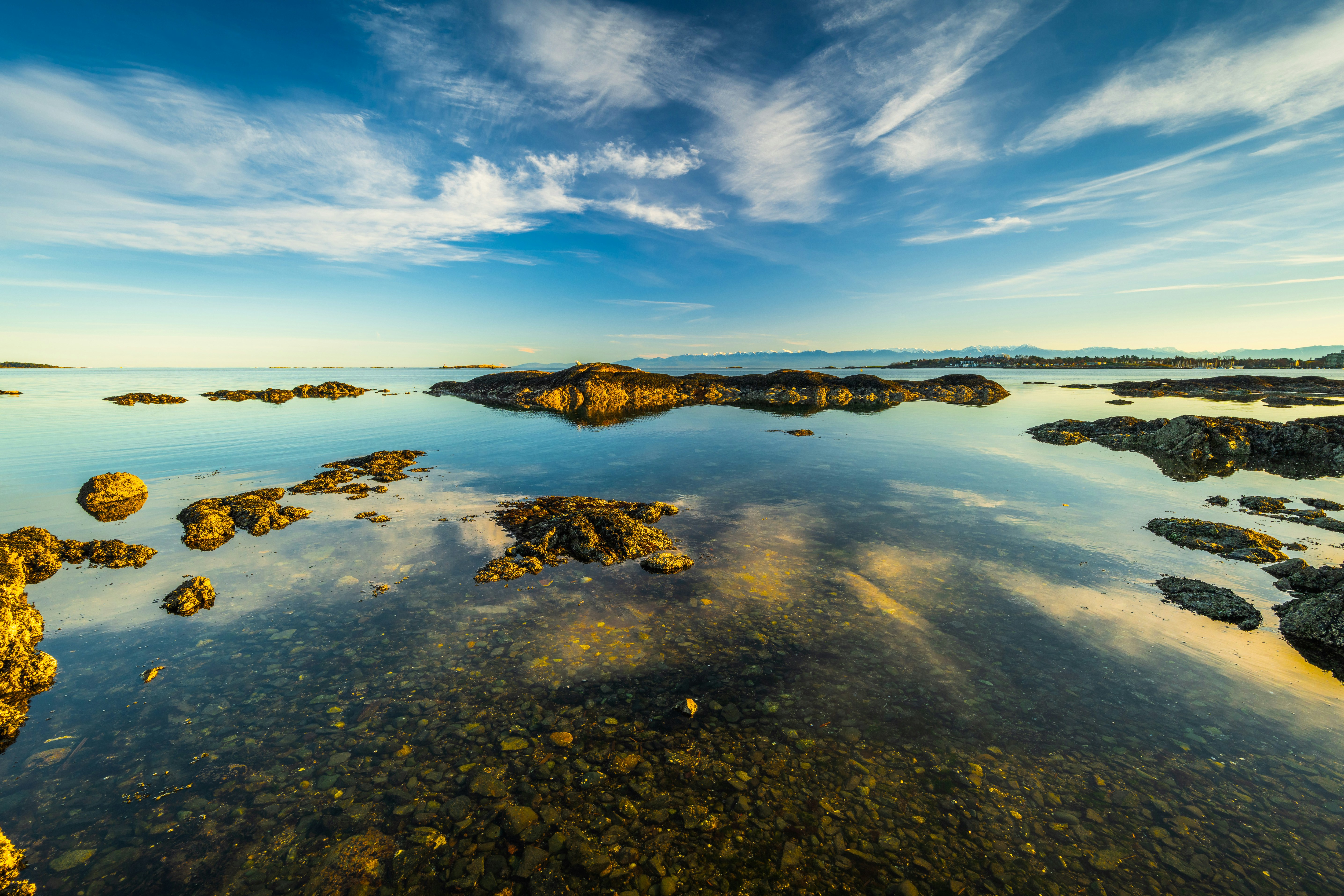 Calm waters reflecting the sky, interspersed with rocky formations along the shoreline. The tranquility of the scene invites contemplation.