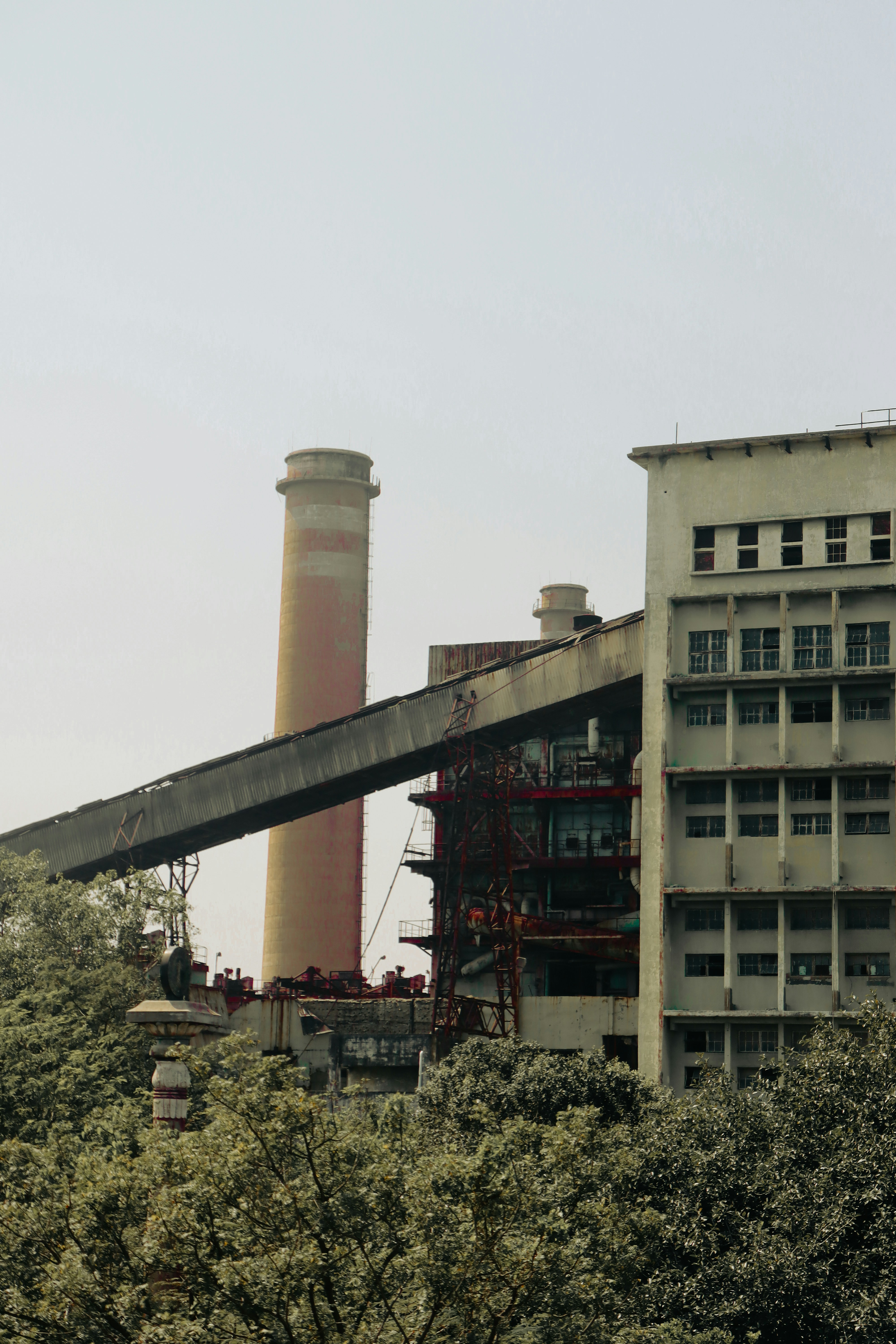 Arc of Industry: The diagonal conveyor threading past a weathered chimney and factory facade