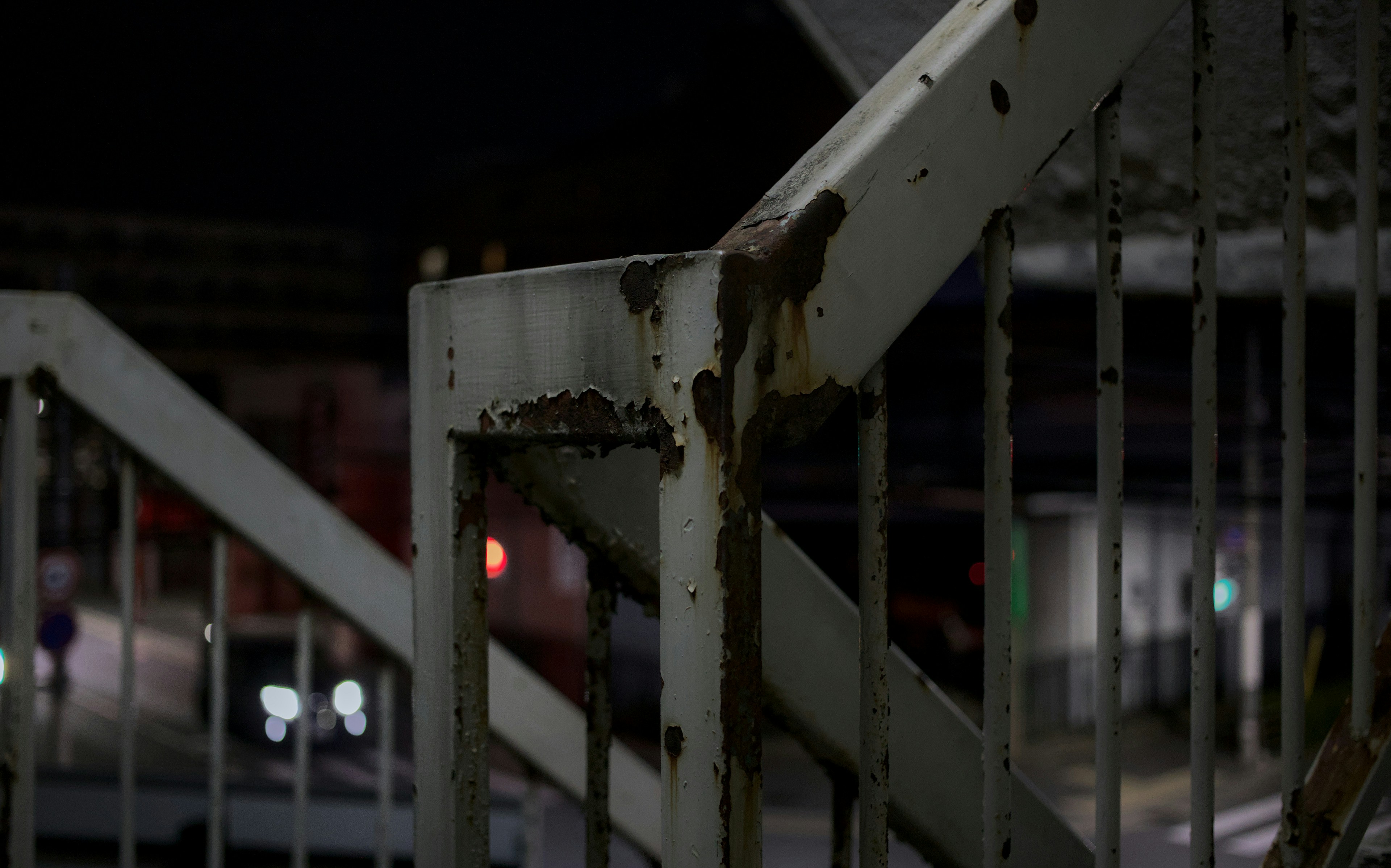 Rusty metal staircase leading down to a dimly lit street at night, highlighting the contrast between urban decay and life beyond. 