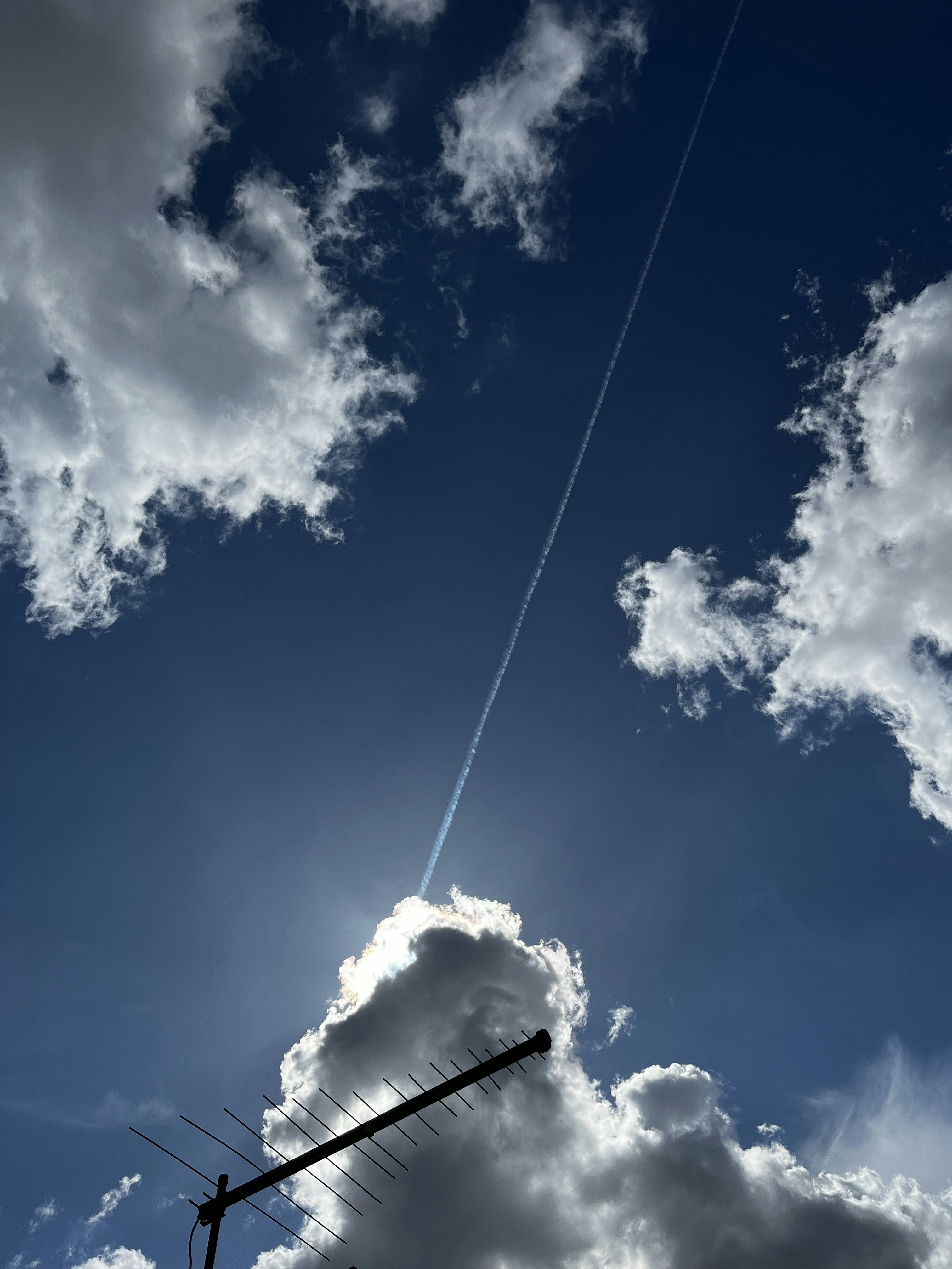 Diagonal Sky Trail Through a Sunlit Cloud, Framed by a Rooftop Antenna