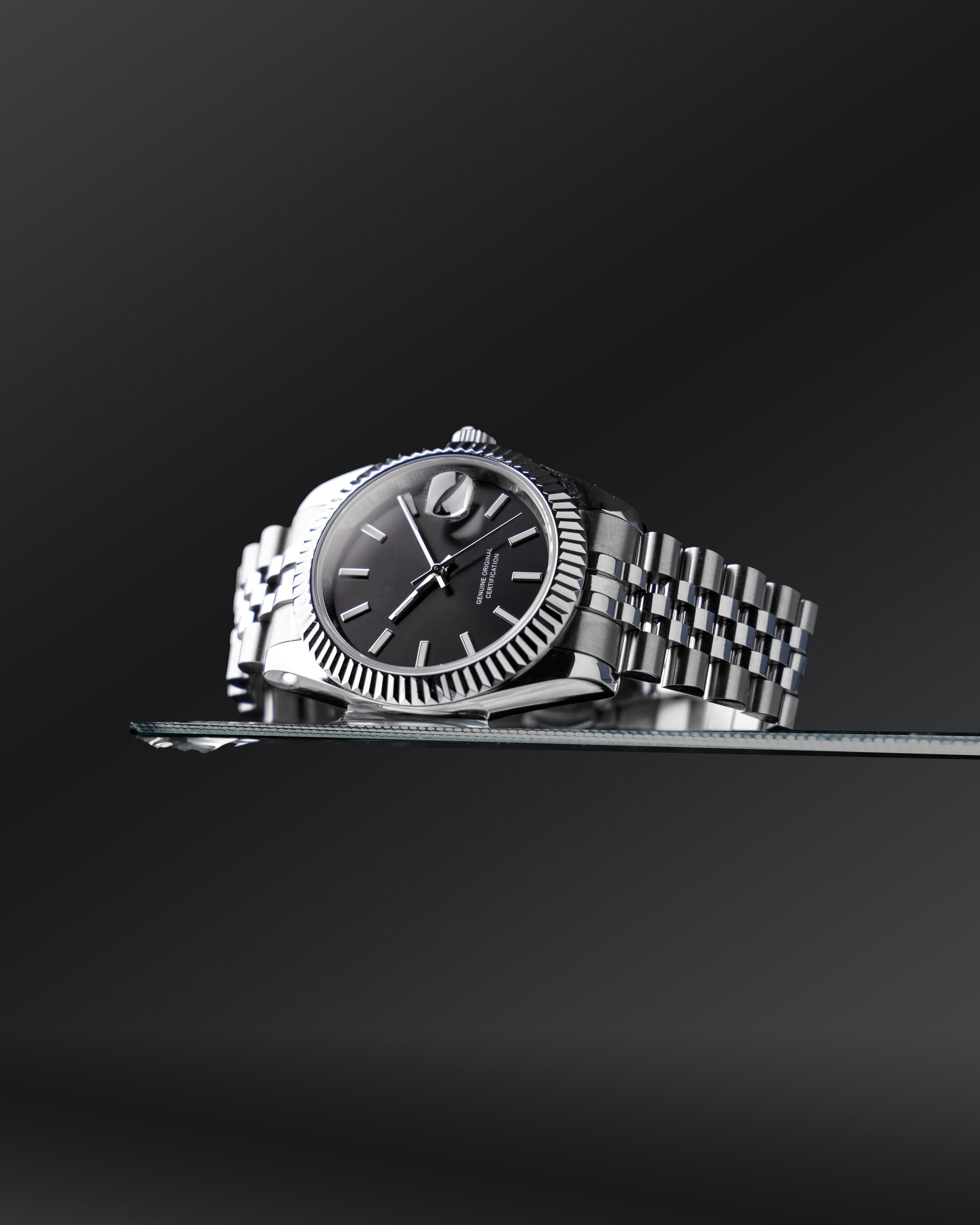 Watch on a piece of glass | a rolex watch on a tray with a black background